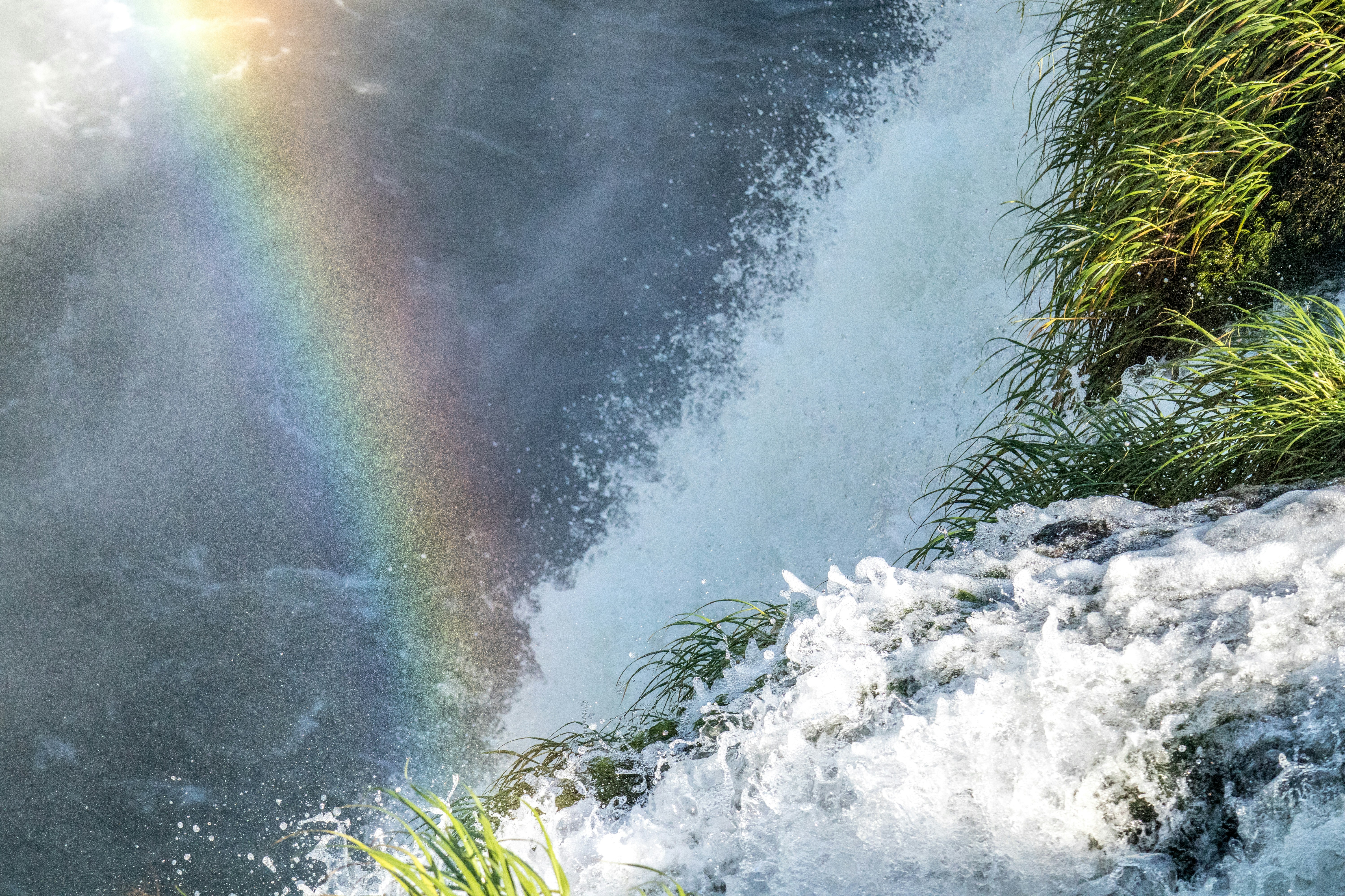 Rainbow over a powerful waterfall with green foliage.