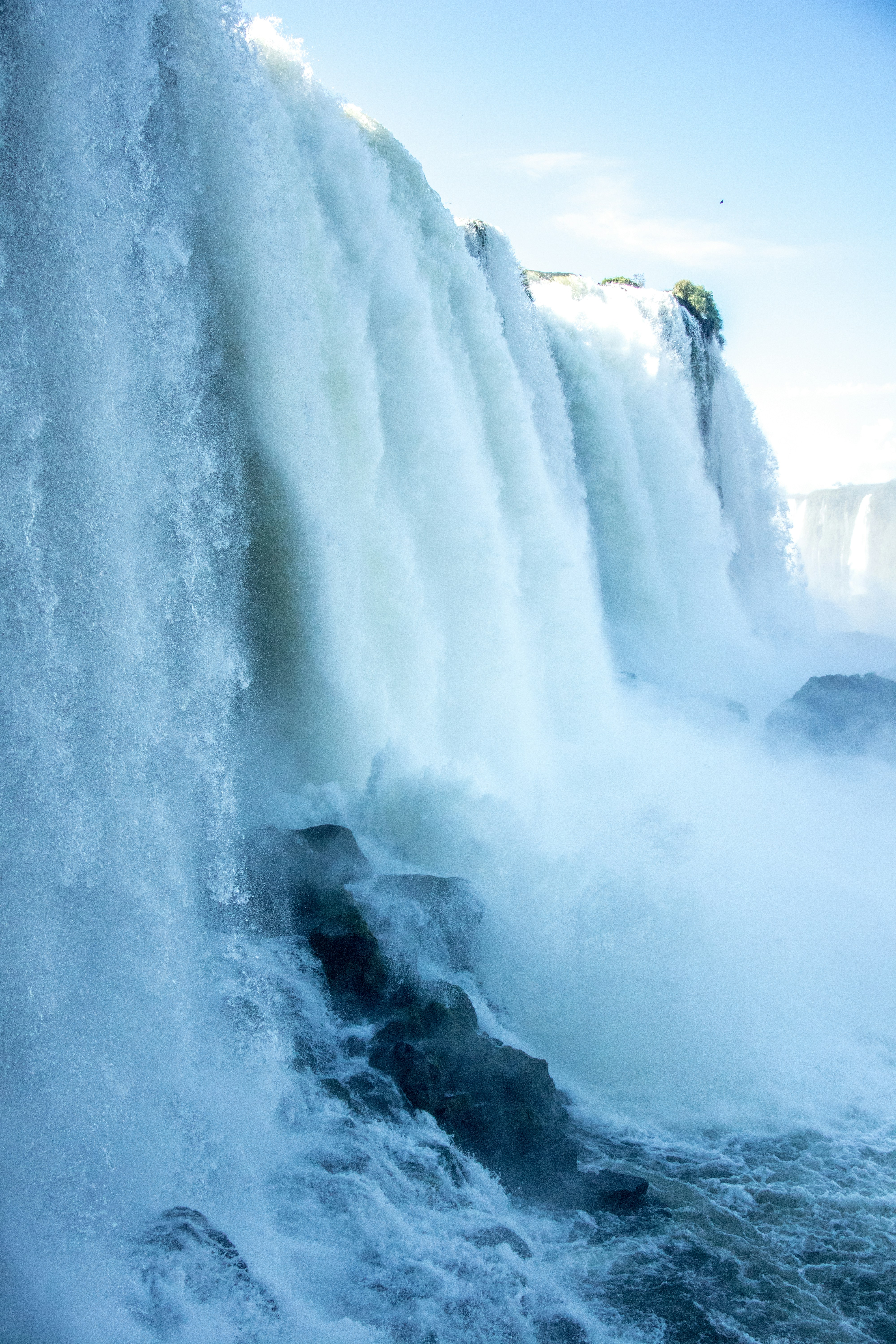 A powerful waterfall cascades over rocks under a bright sky.