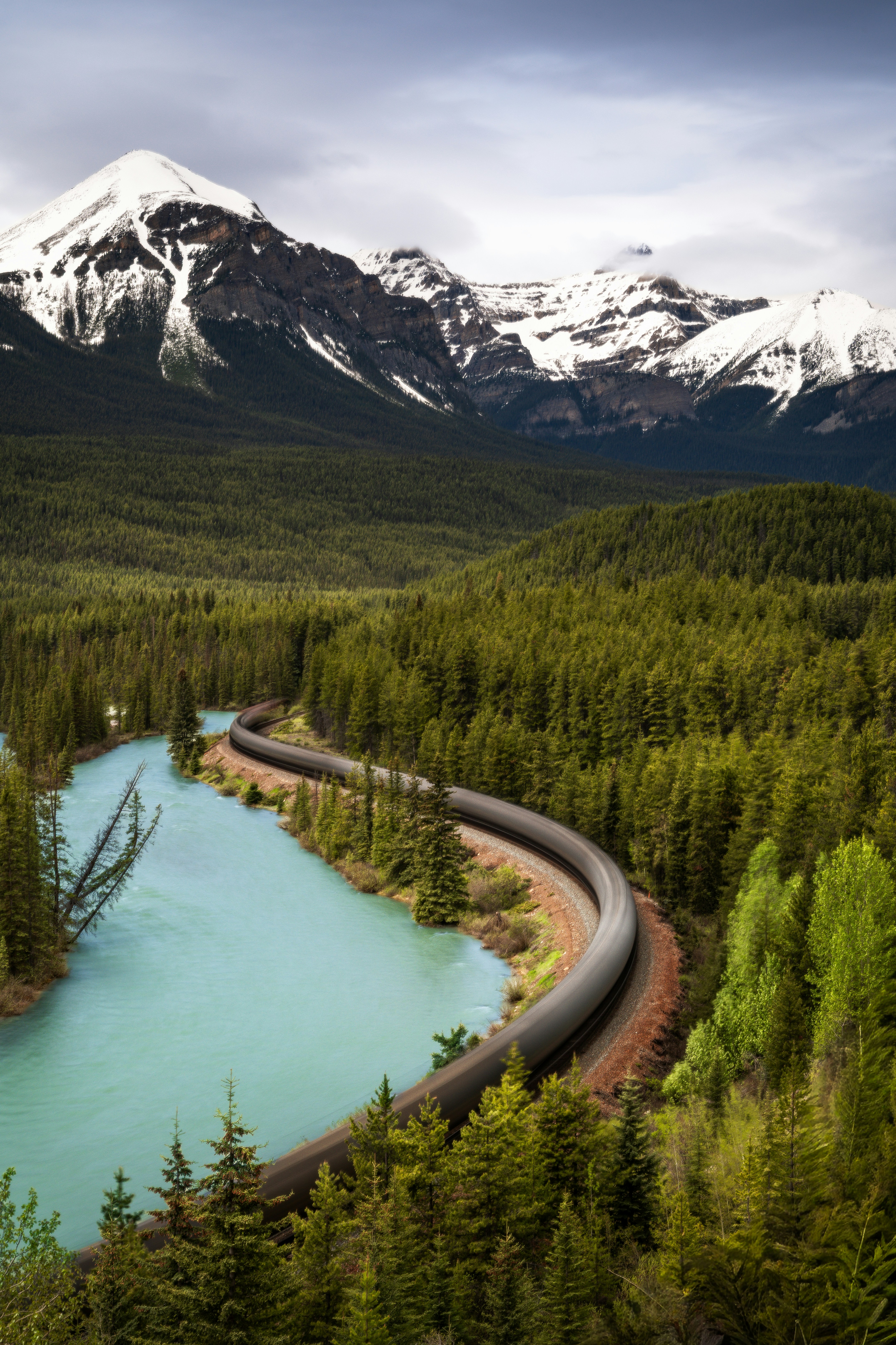 Snow-Capped Peaks Guard the Winding Rail along a Teal River