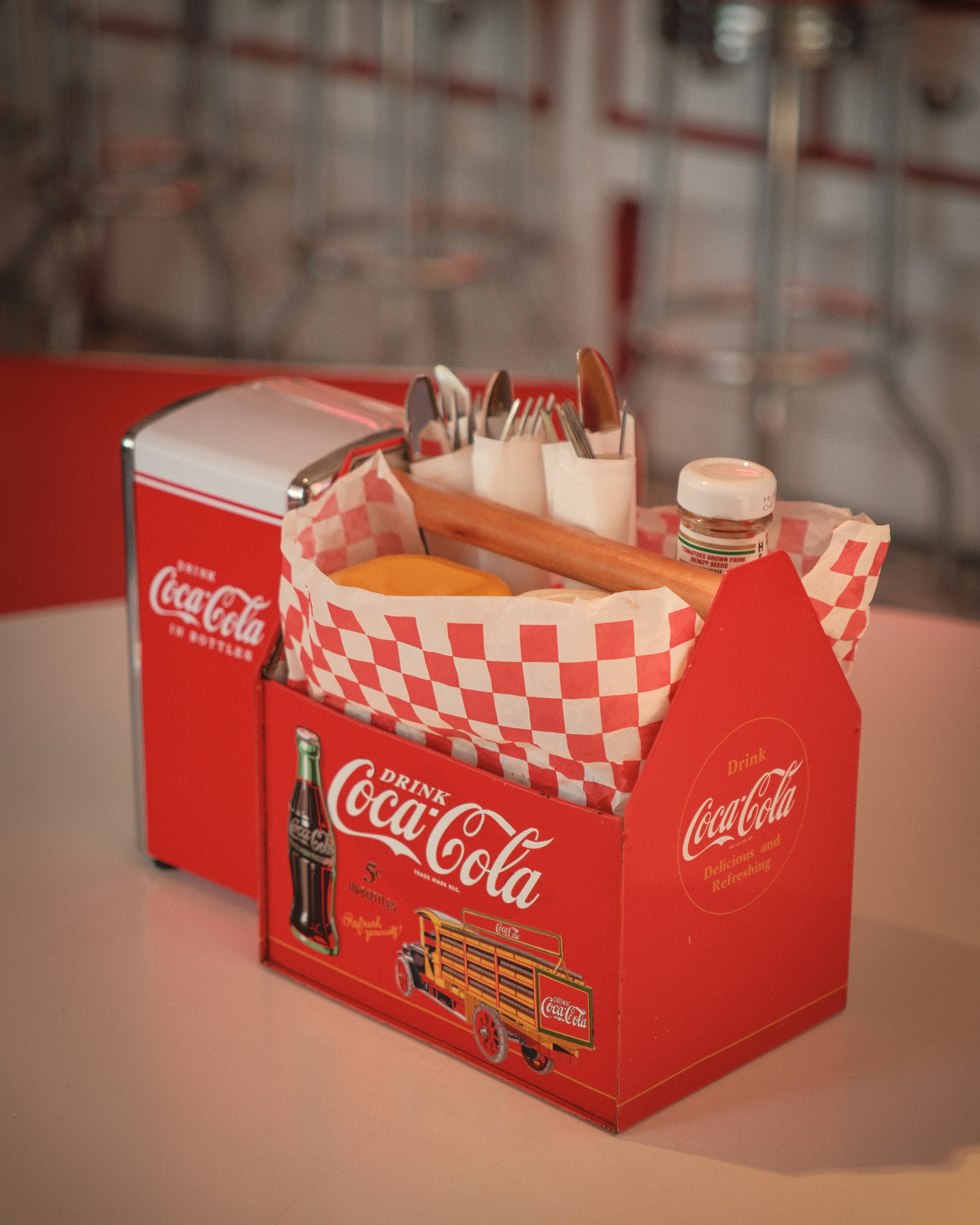 Coca-cola napkin dispenser and utensil caddy on a table.