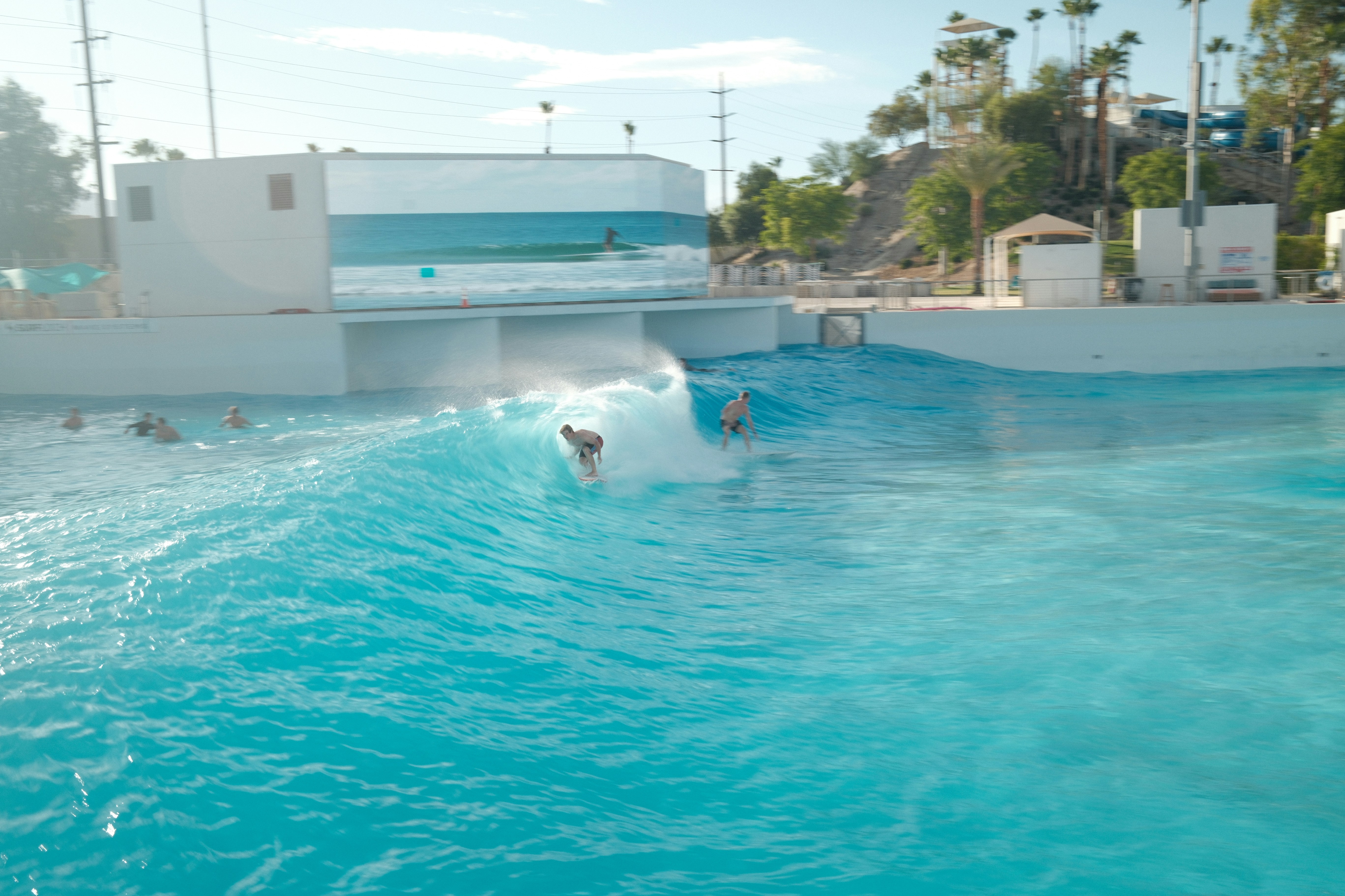 Surfer riding a bright blue wave in a wave pool.