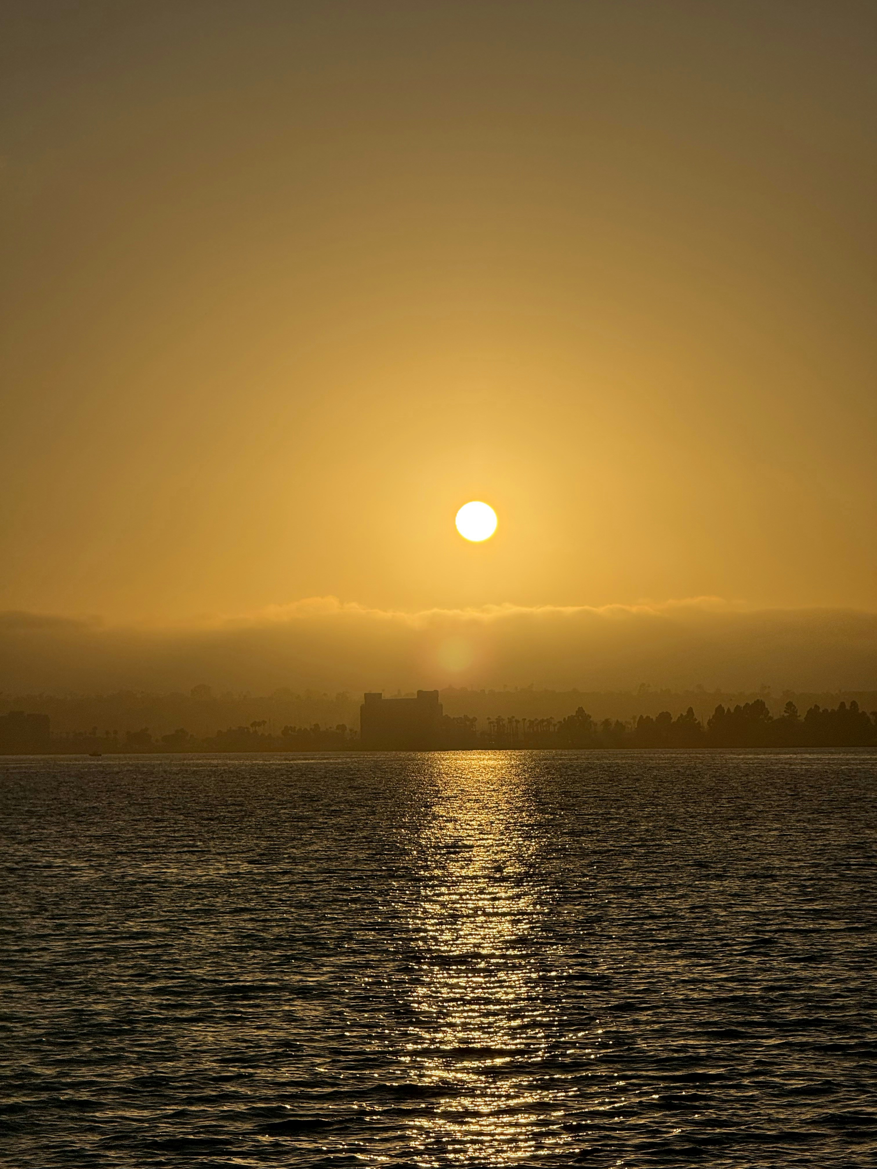 Golden sunset over the ocean with distant city silhouette.