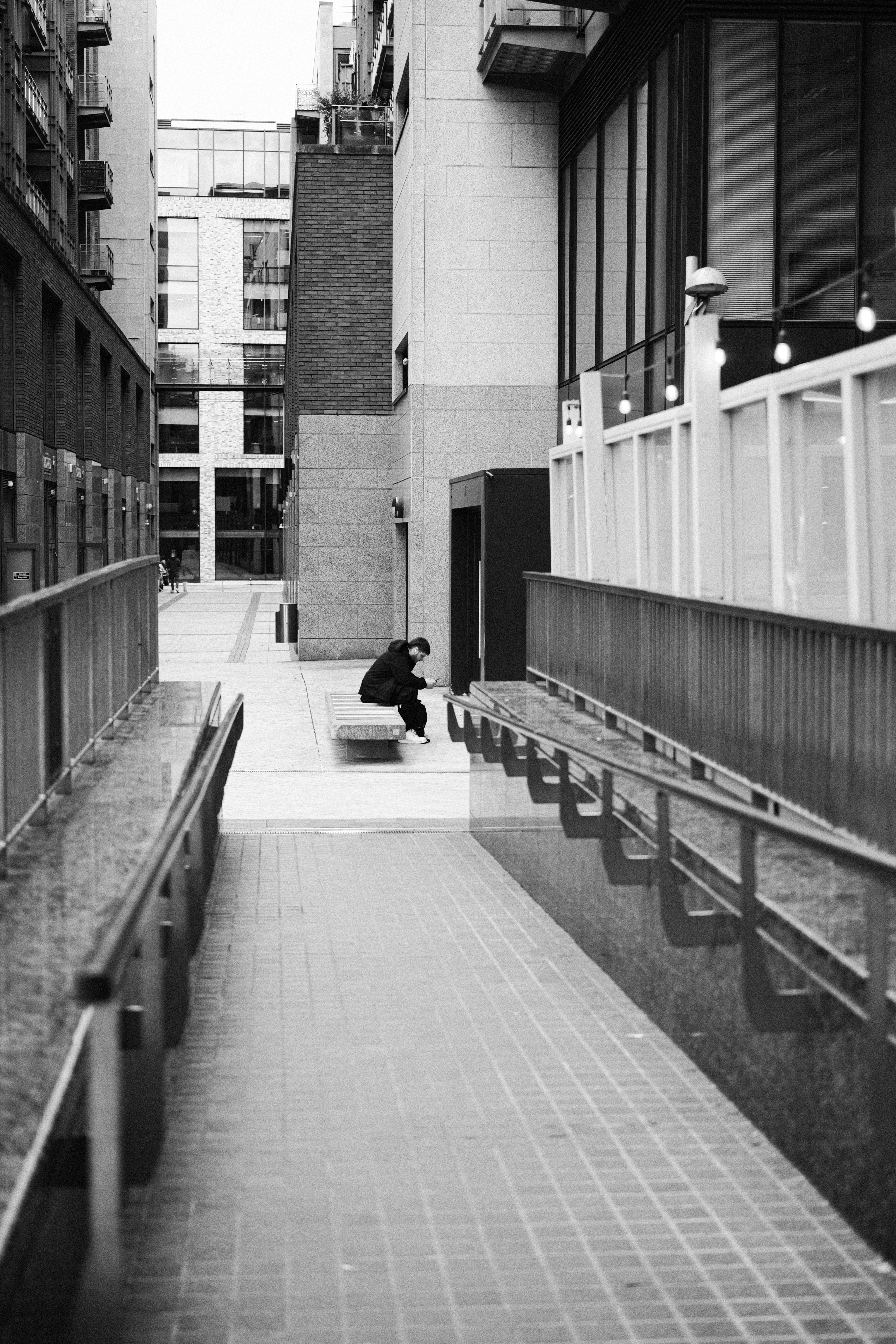 Urban Solitude: A Figure on the Concrete Bench Between Glass and Rail