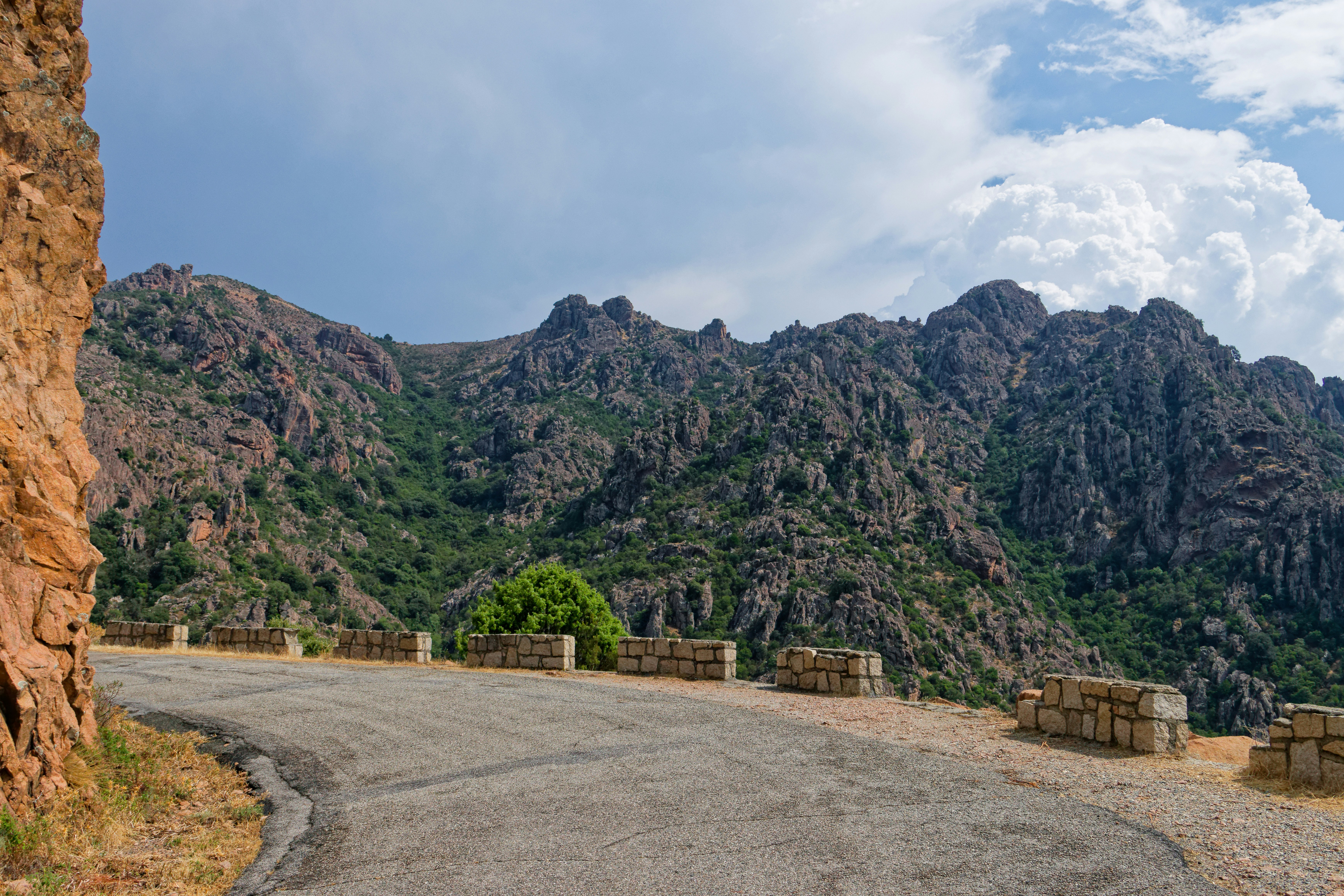 Winding mountain road with rocky peaks under a cloudy sky.
