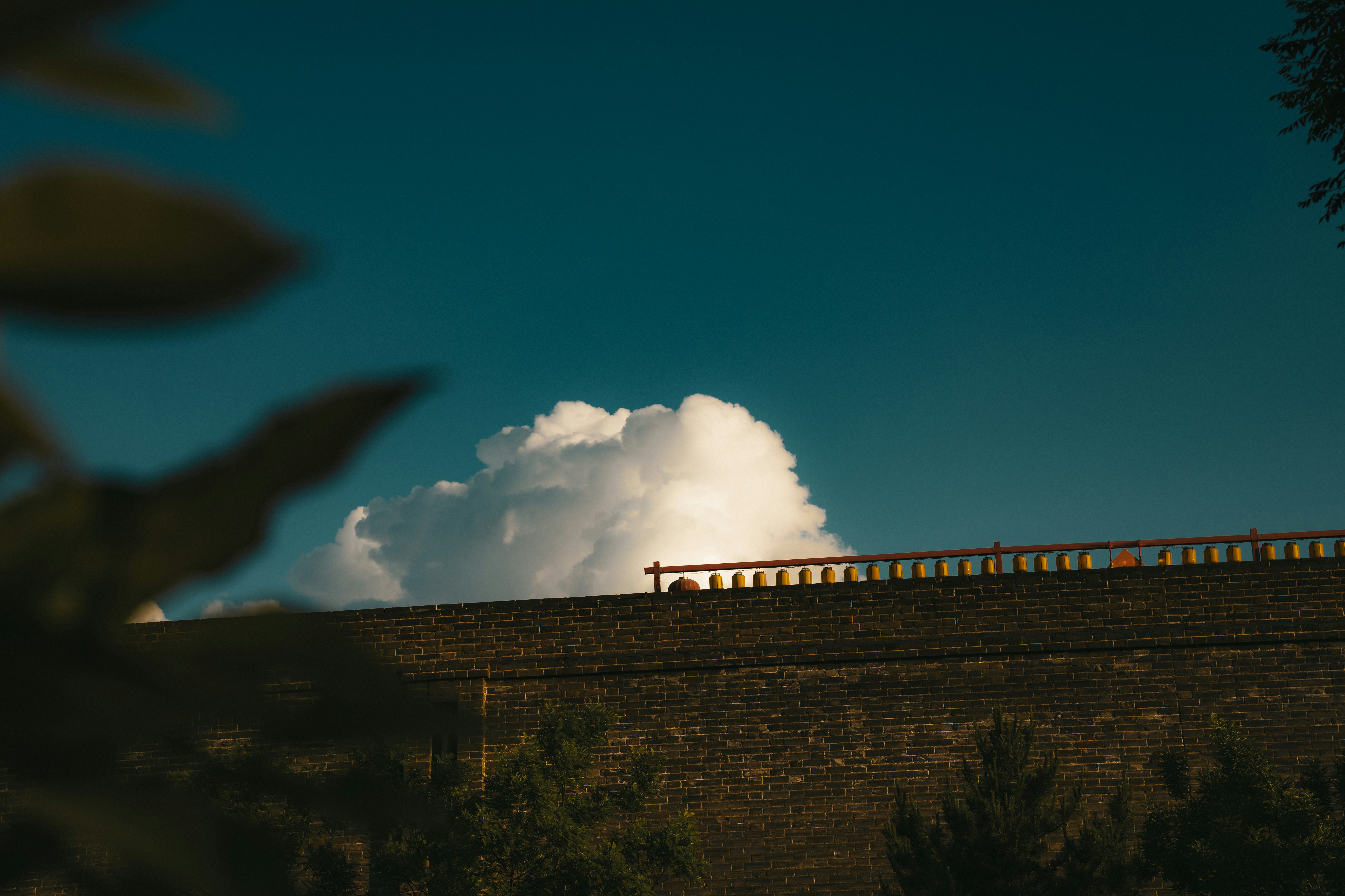 White cloud against blue sky above a dark stone wall.