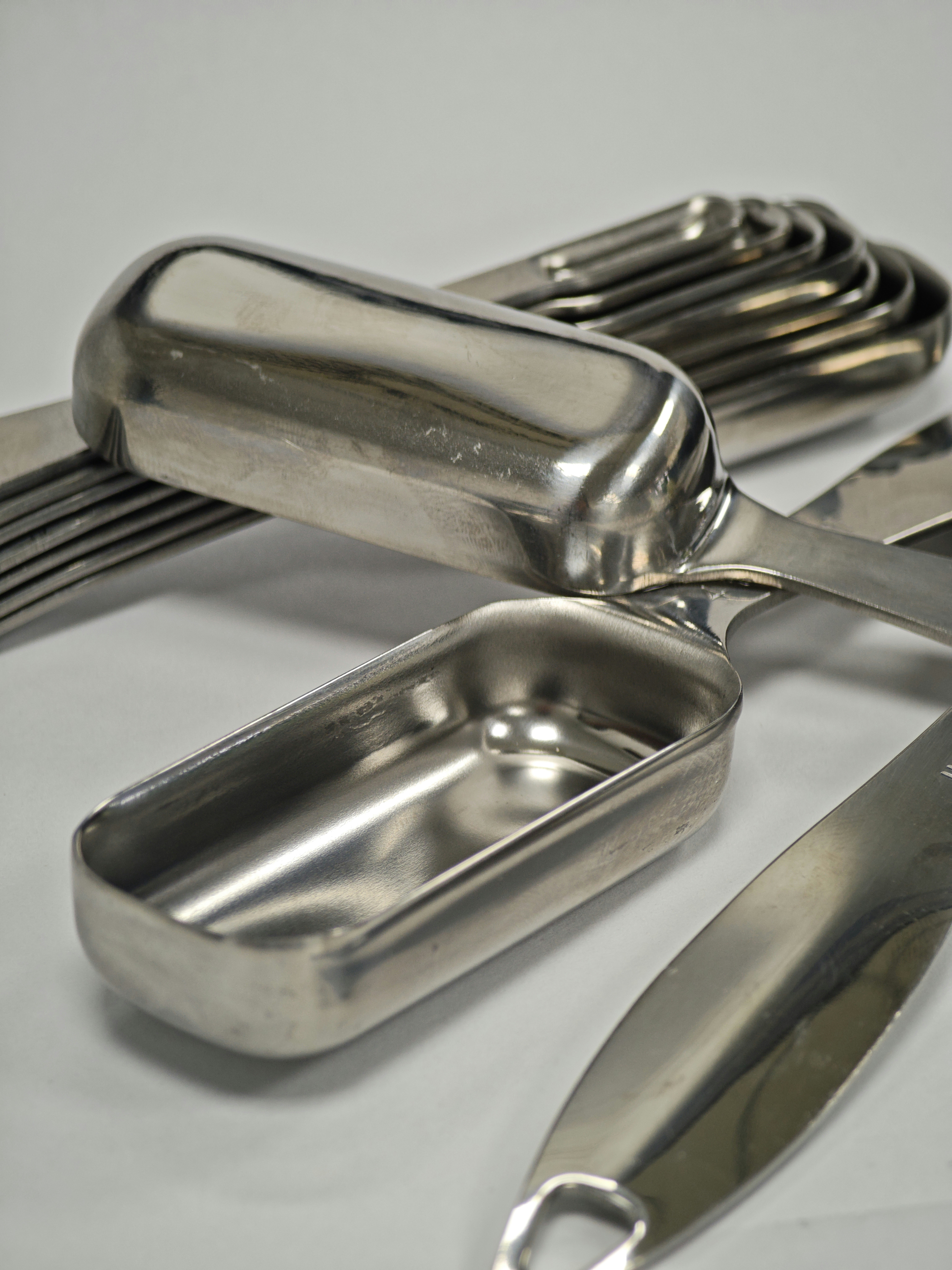 Shiny metal utensils arranged in a stack with a raised lid, emphasizing reflections and metallic texture in a minimal still life.
