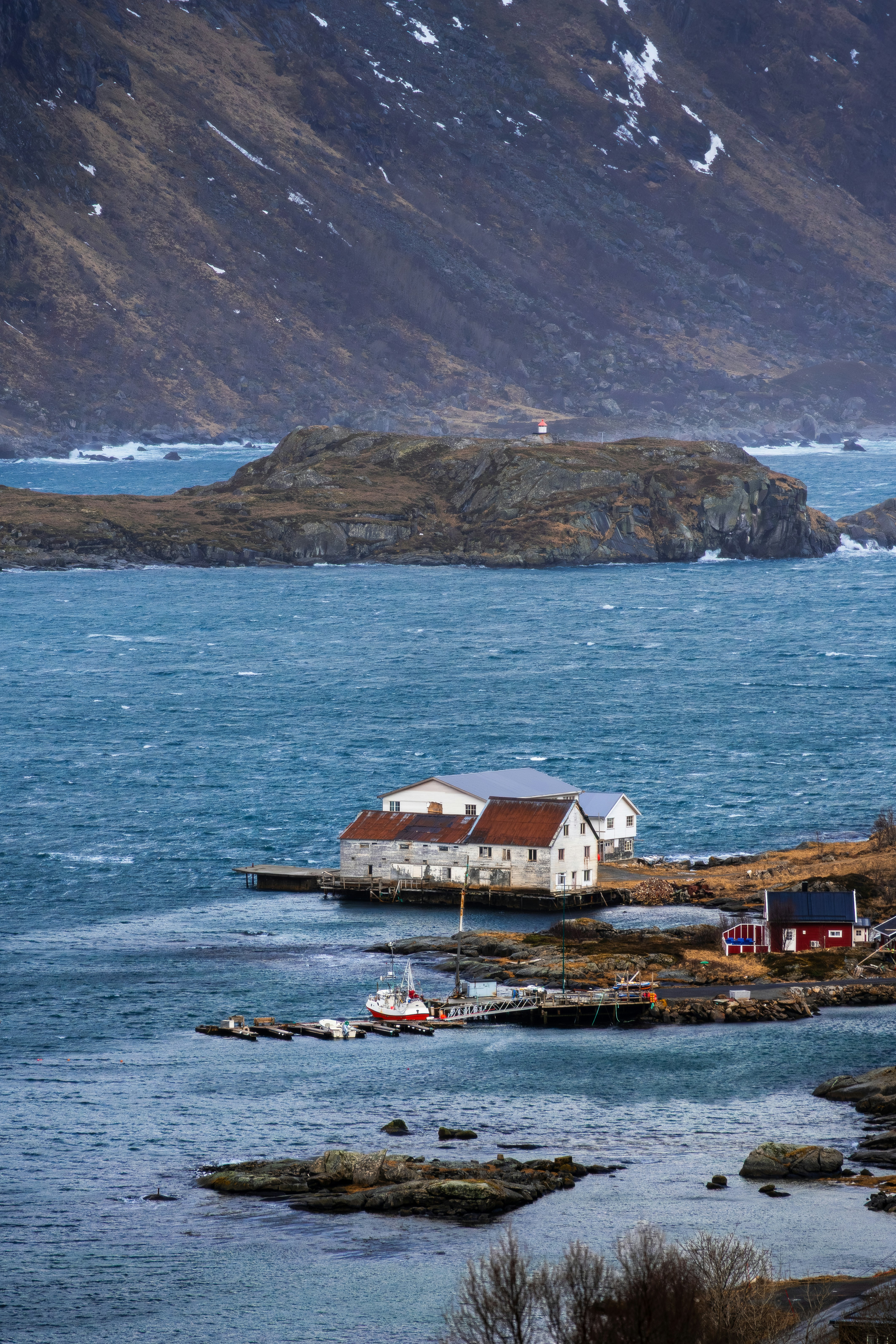 White buildings on a stormy coast with distant snowy mountains.