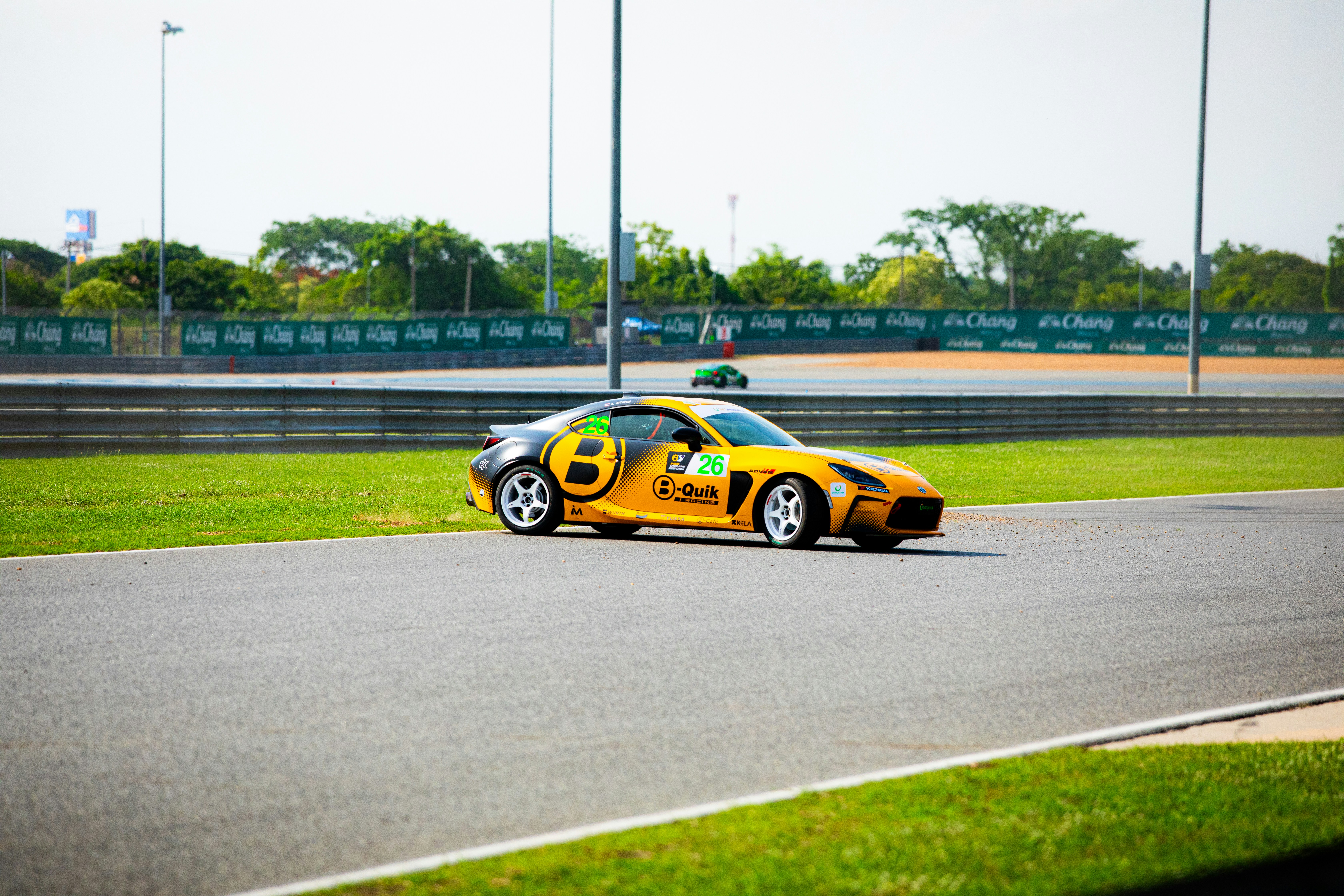 Yellow race car on sunlit track escapes into a blur of green and asphalt
