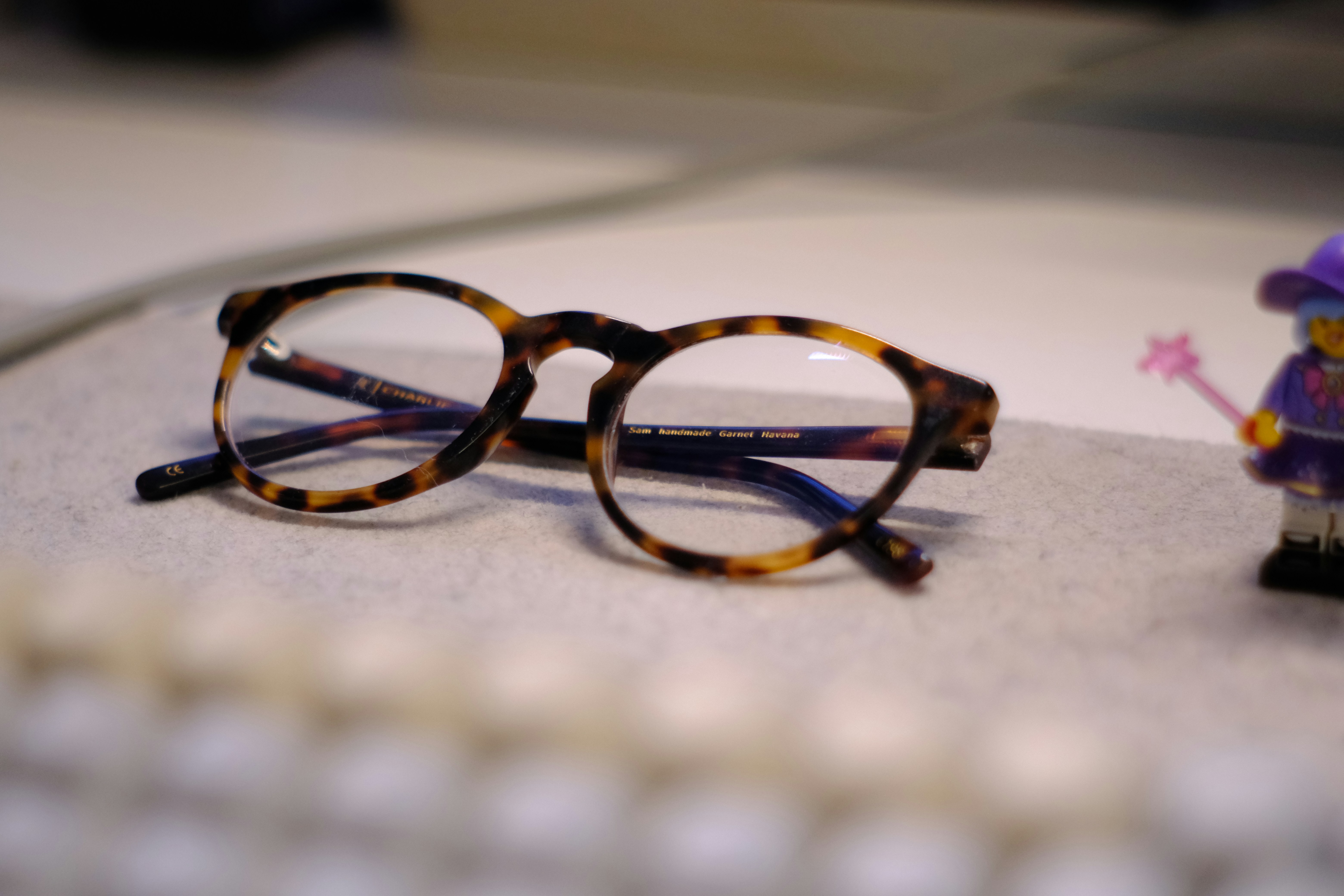 Tortoiseshell Glasses Resting on a Soft Desk, Beneath a Tiny Toy Figure
