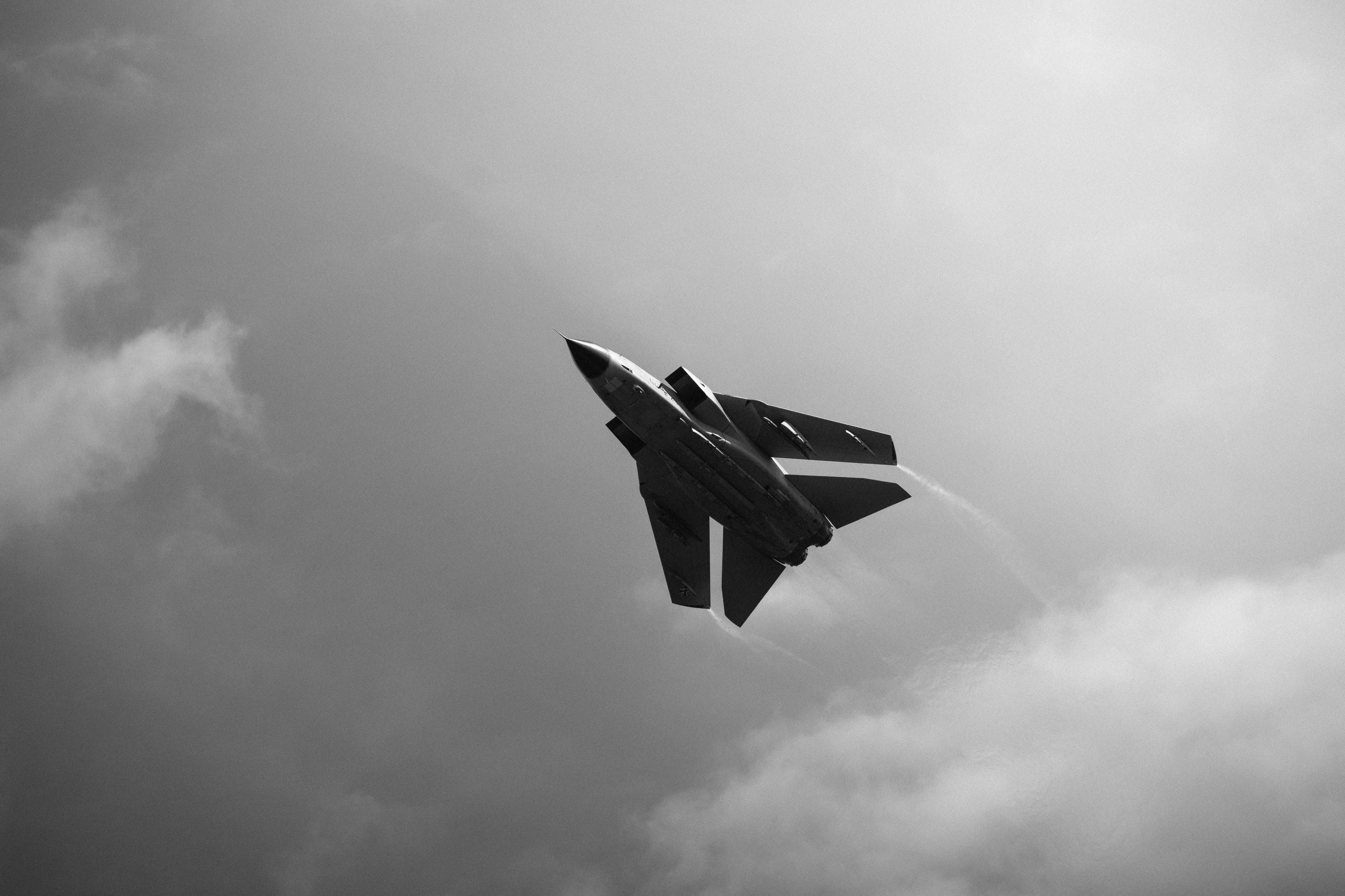 Black and white fighter jet soaring through the clouds.