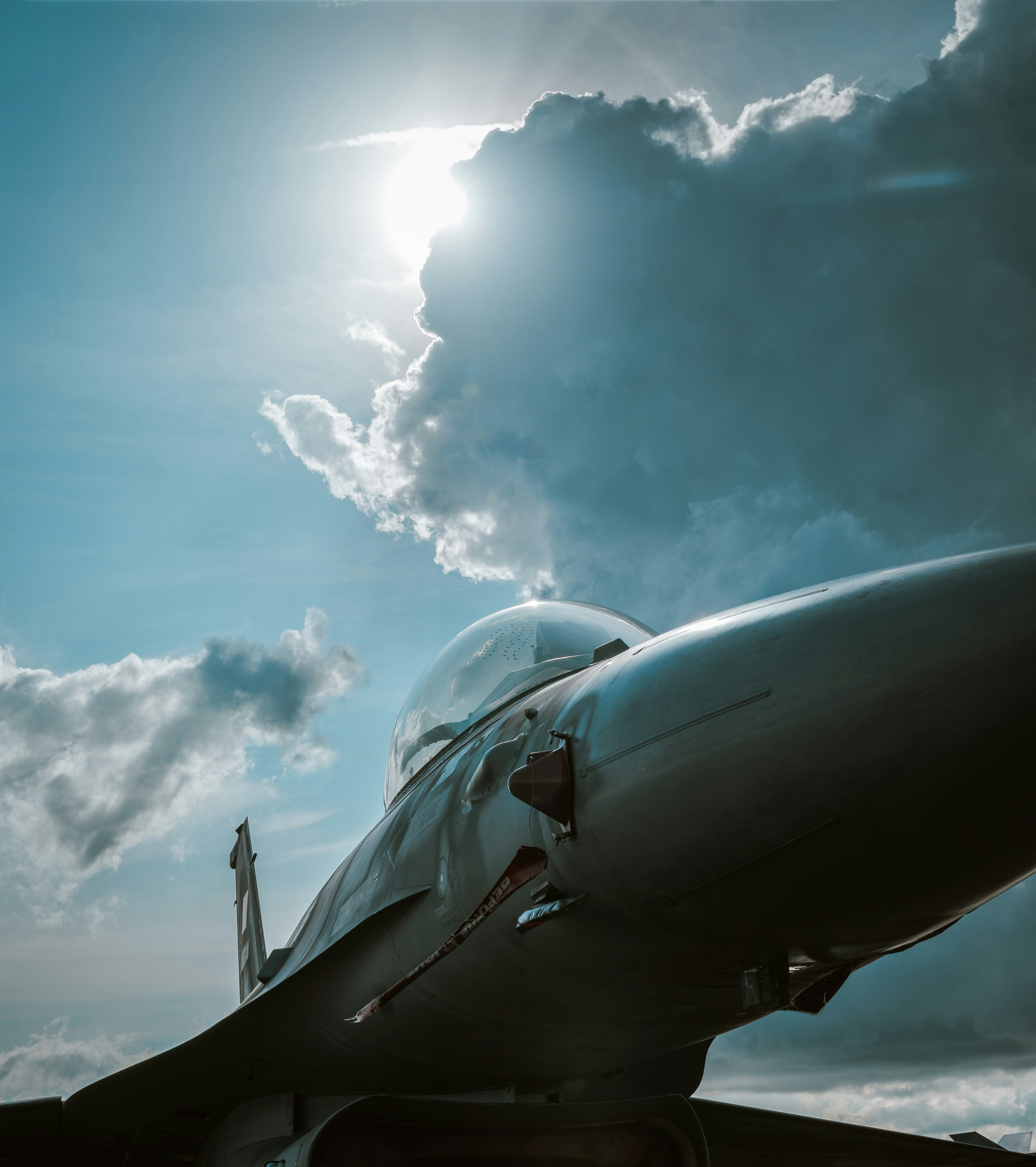 A fighter jet against a bright, cloudy sky.