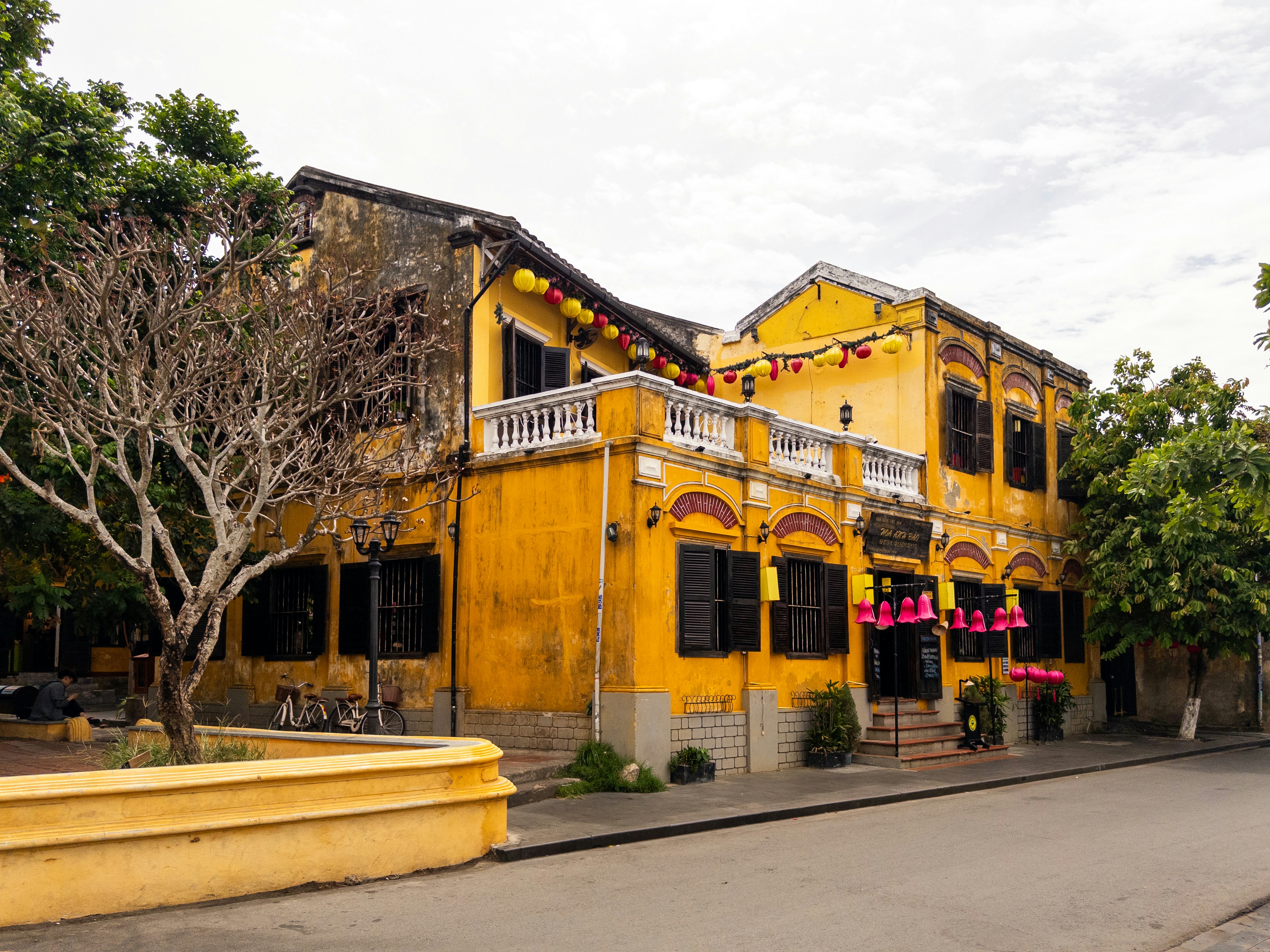 Historic yellow building with dark windows and a leafless tree.