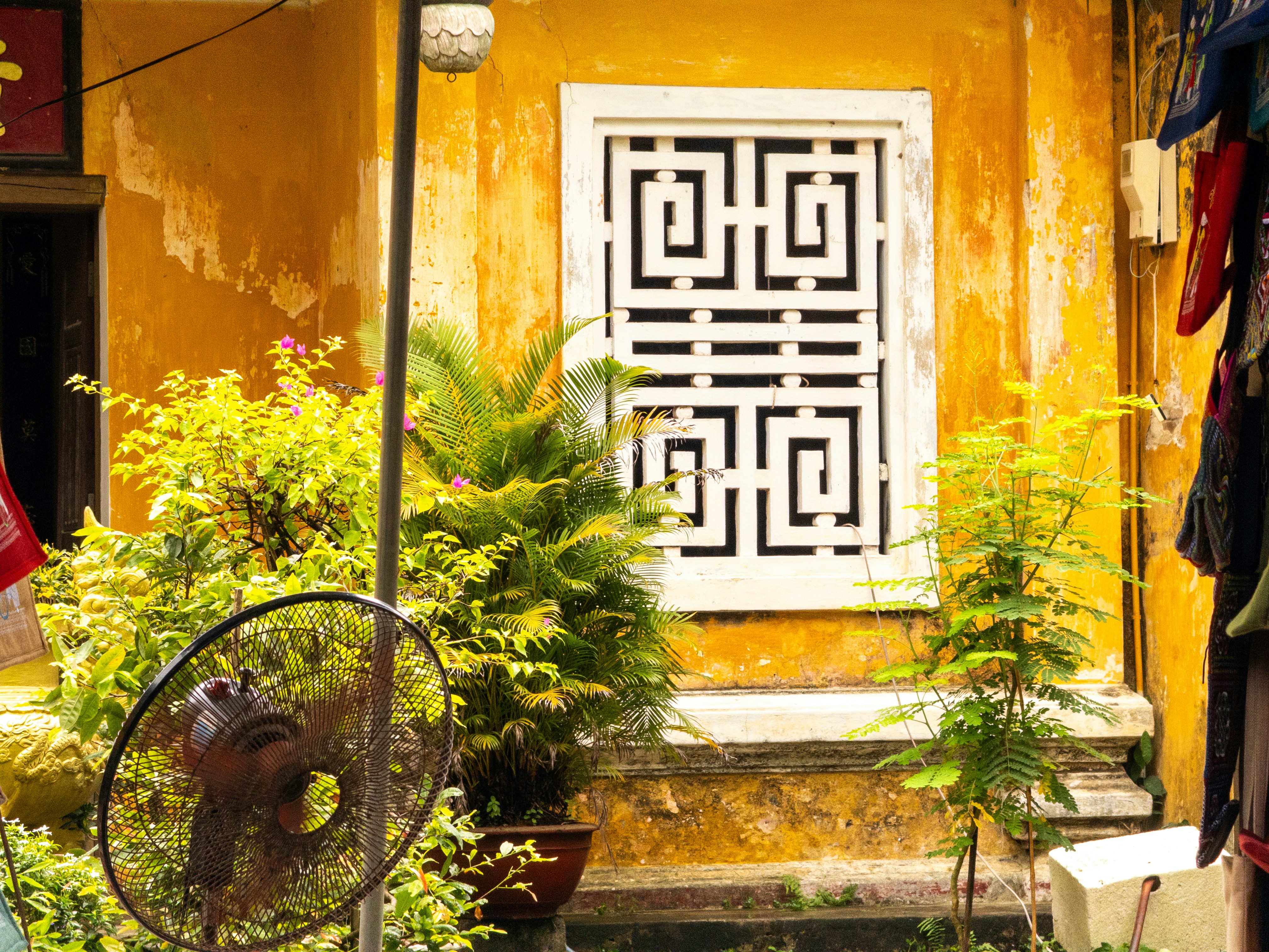Sunlit Yellow Courtyard with Ornate Window and Fan
