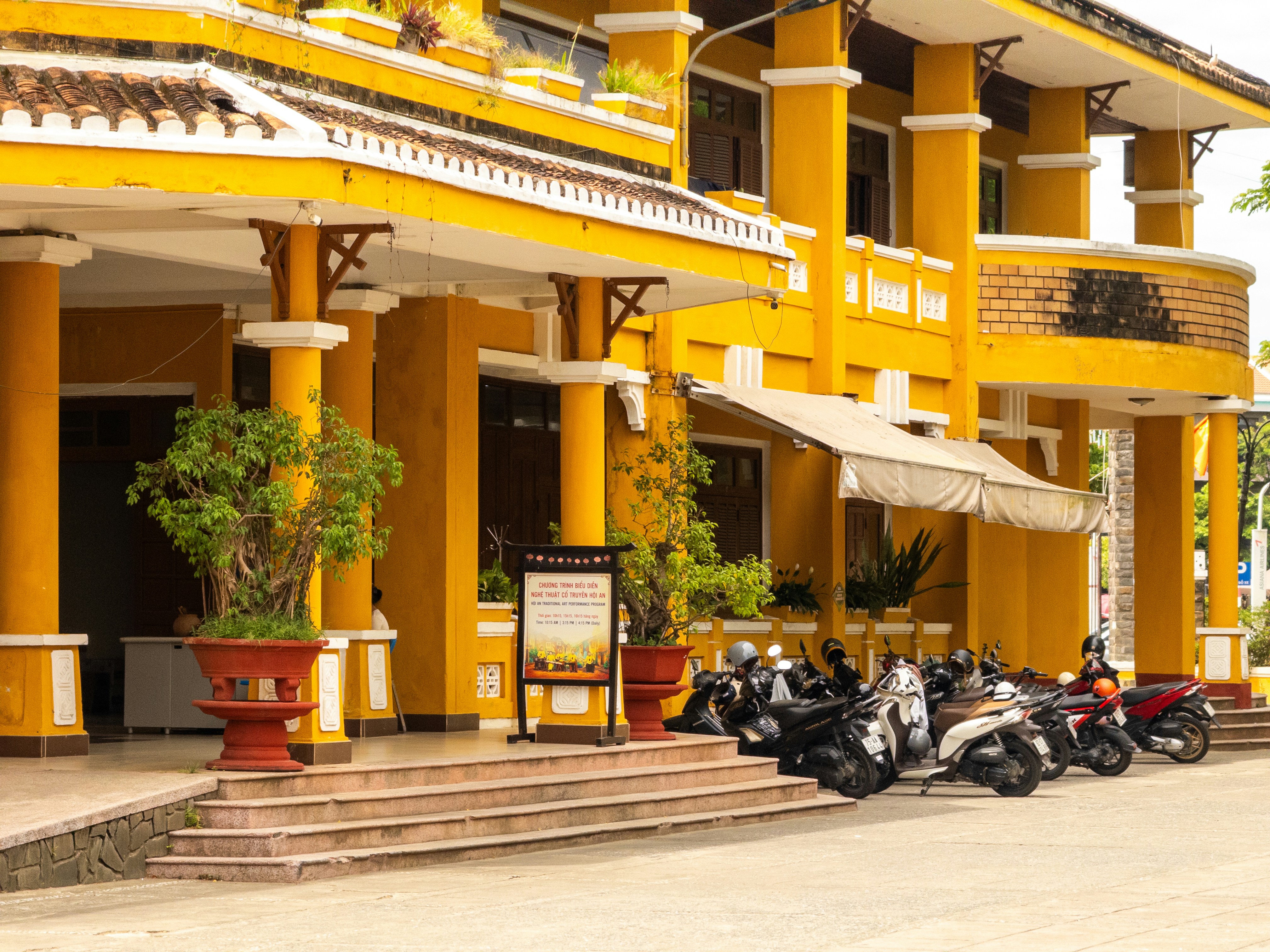 Yellow asian-style building with parked motorbikes and potted plants.