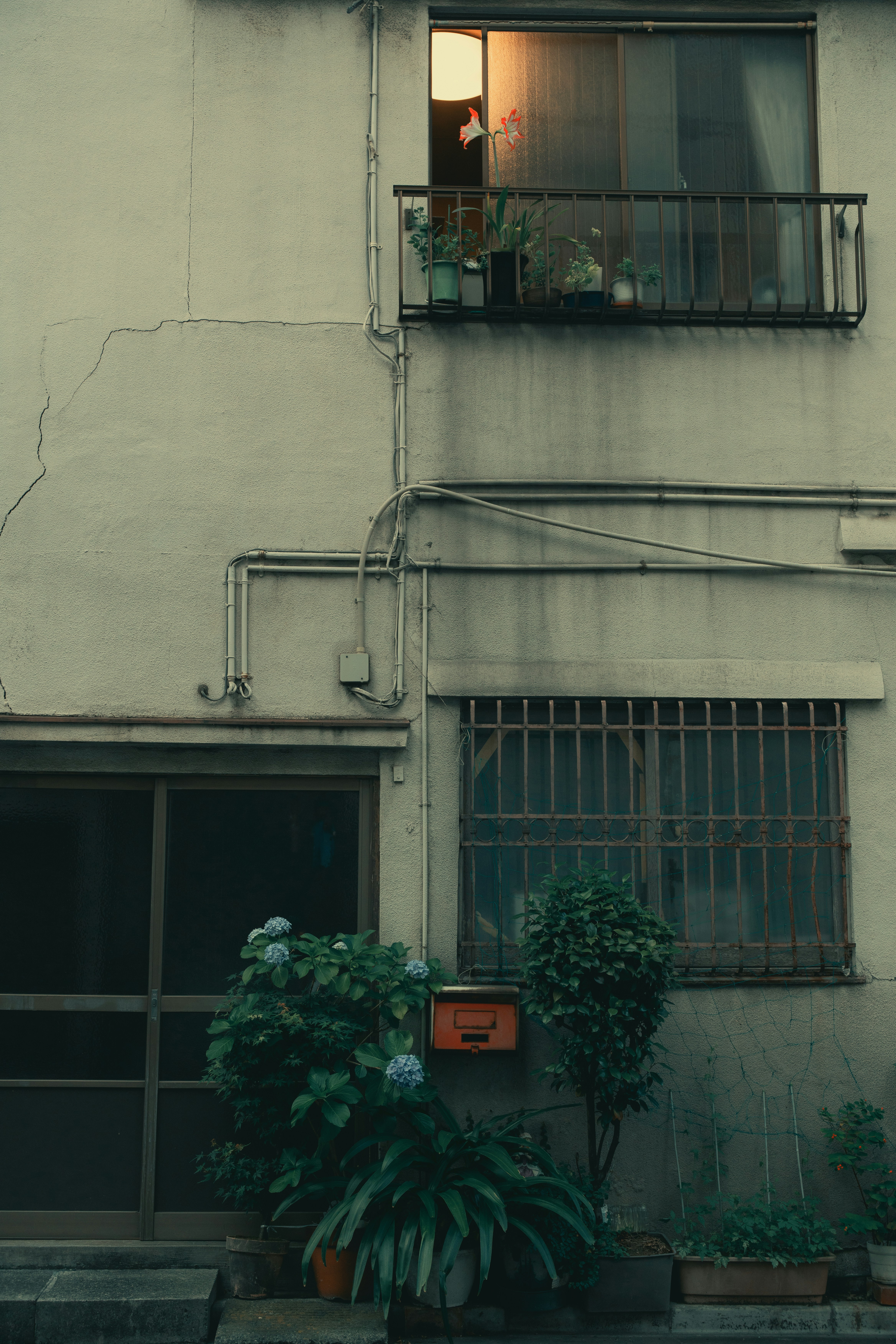 Old building with balcony, glowing window, and potted plants.