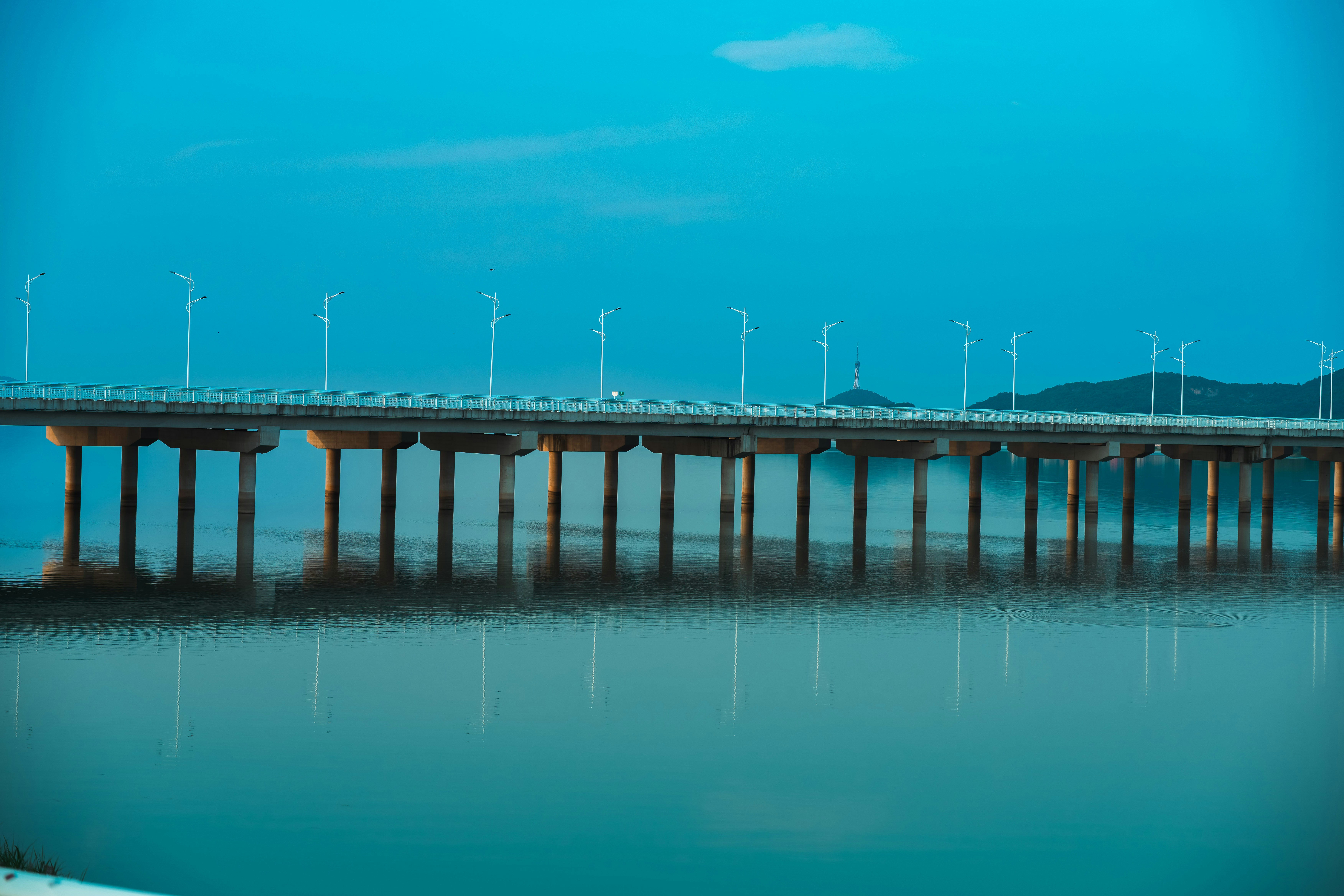A long bridge with streetlights over calm water at twilight.