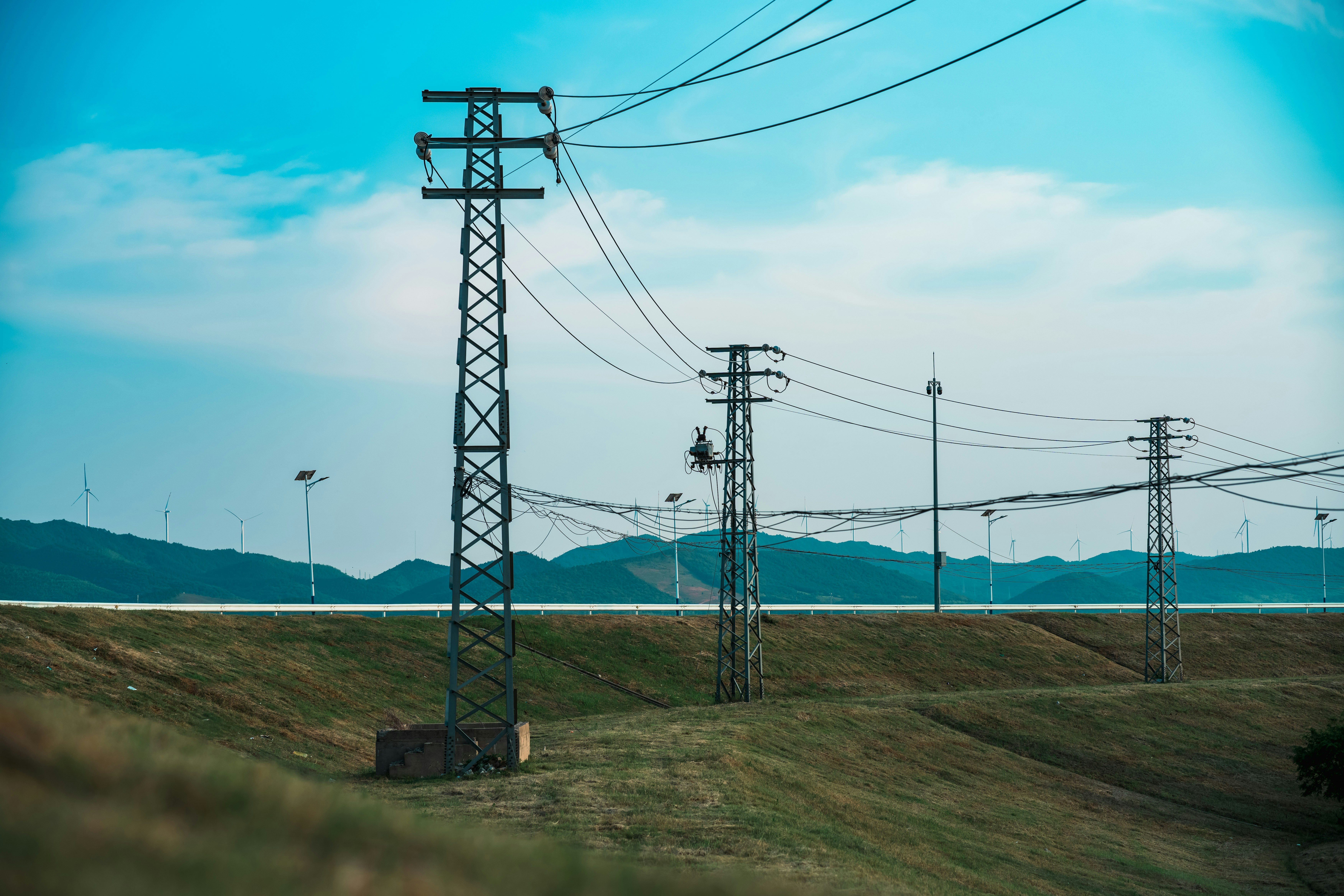 Electricity pylons on a grassy hill under a blue sky.