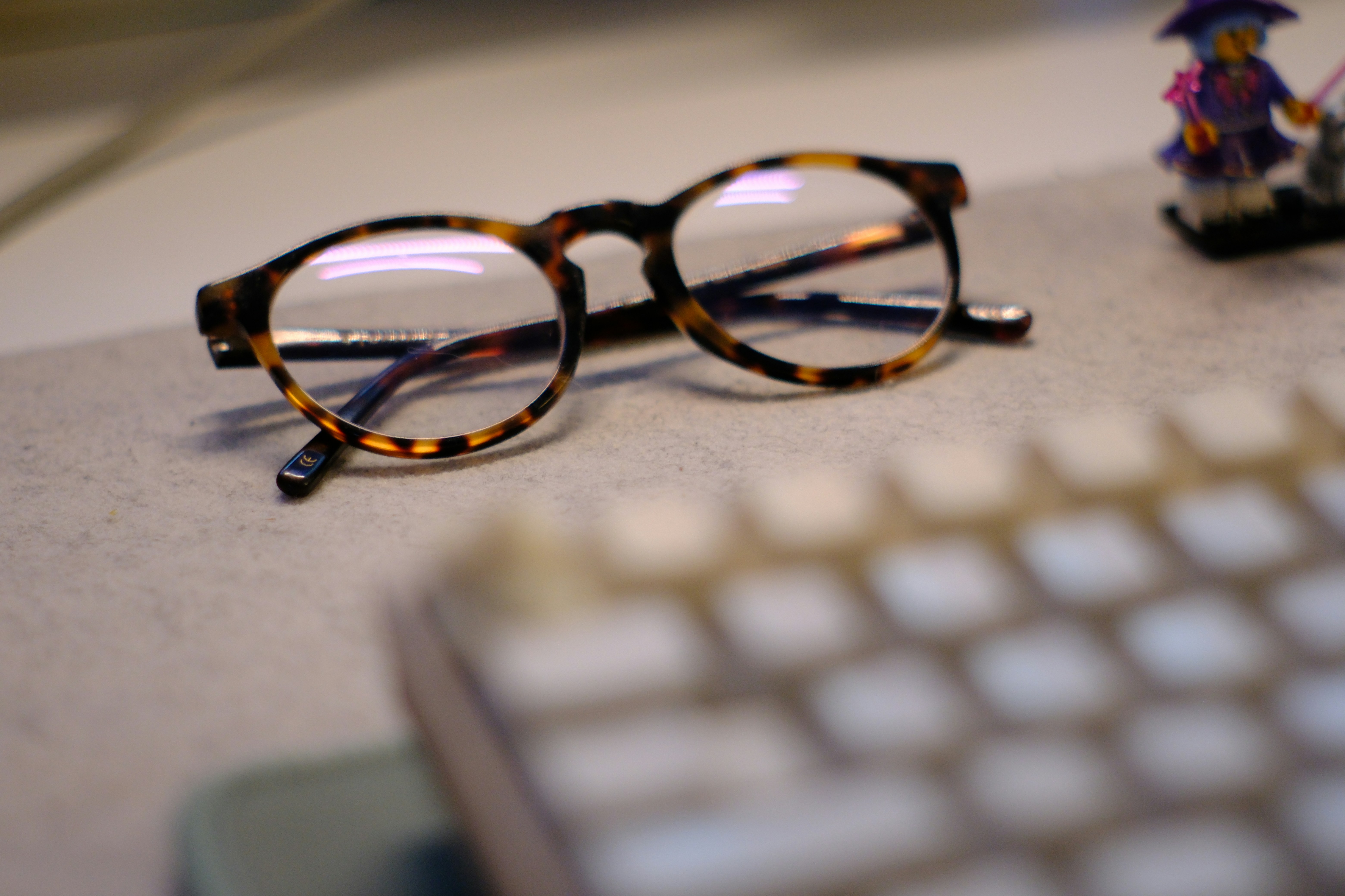 Tortoiseshell glasses resting on a desk with a blurred keyboard.