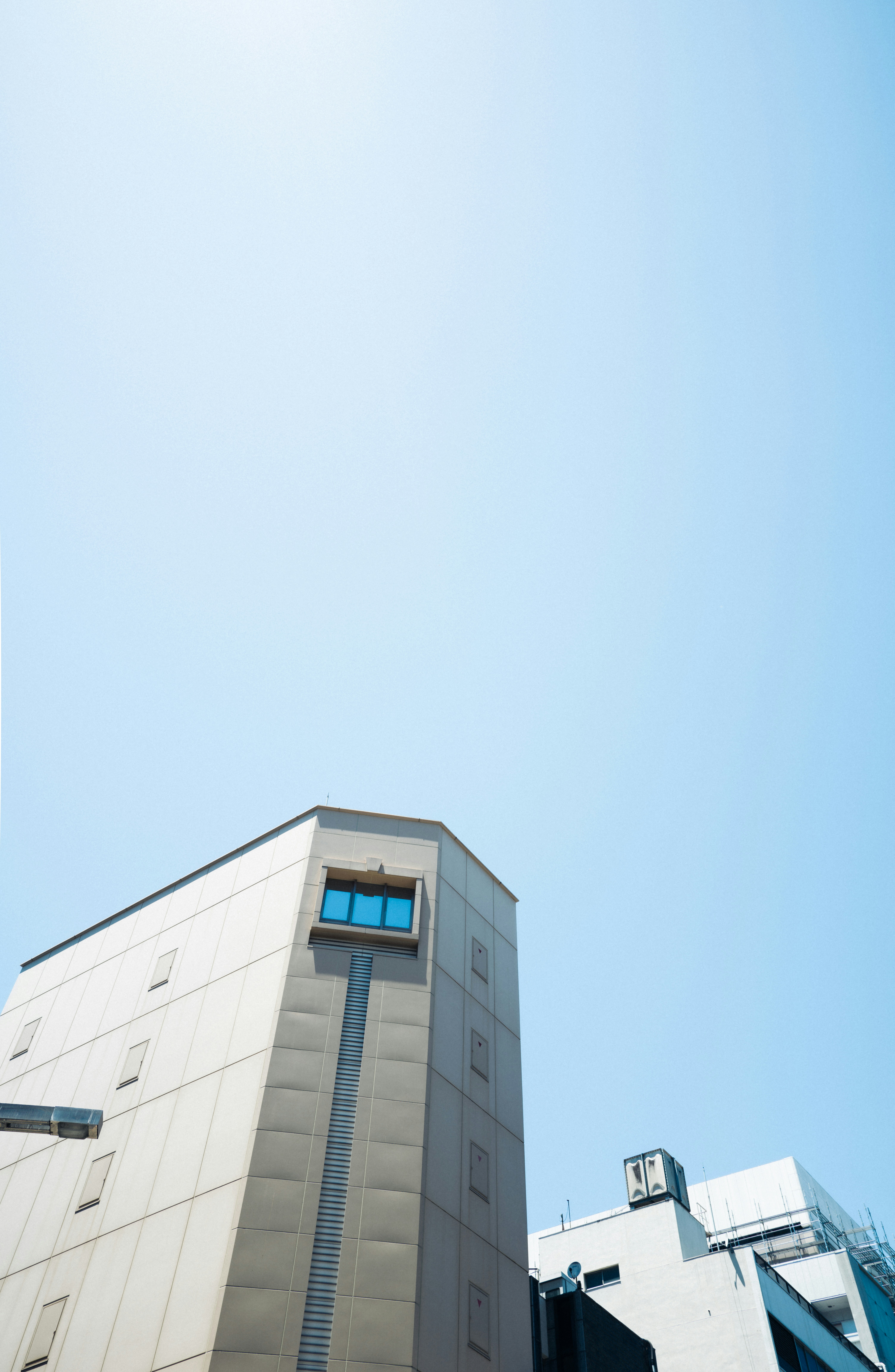 Tall building with a blue window against a clear sky.