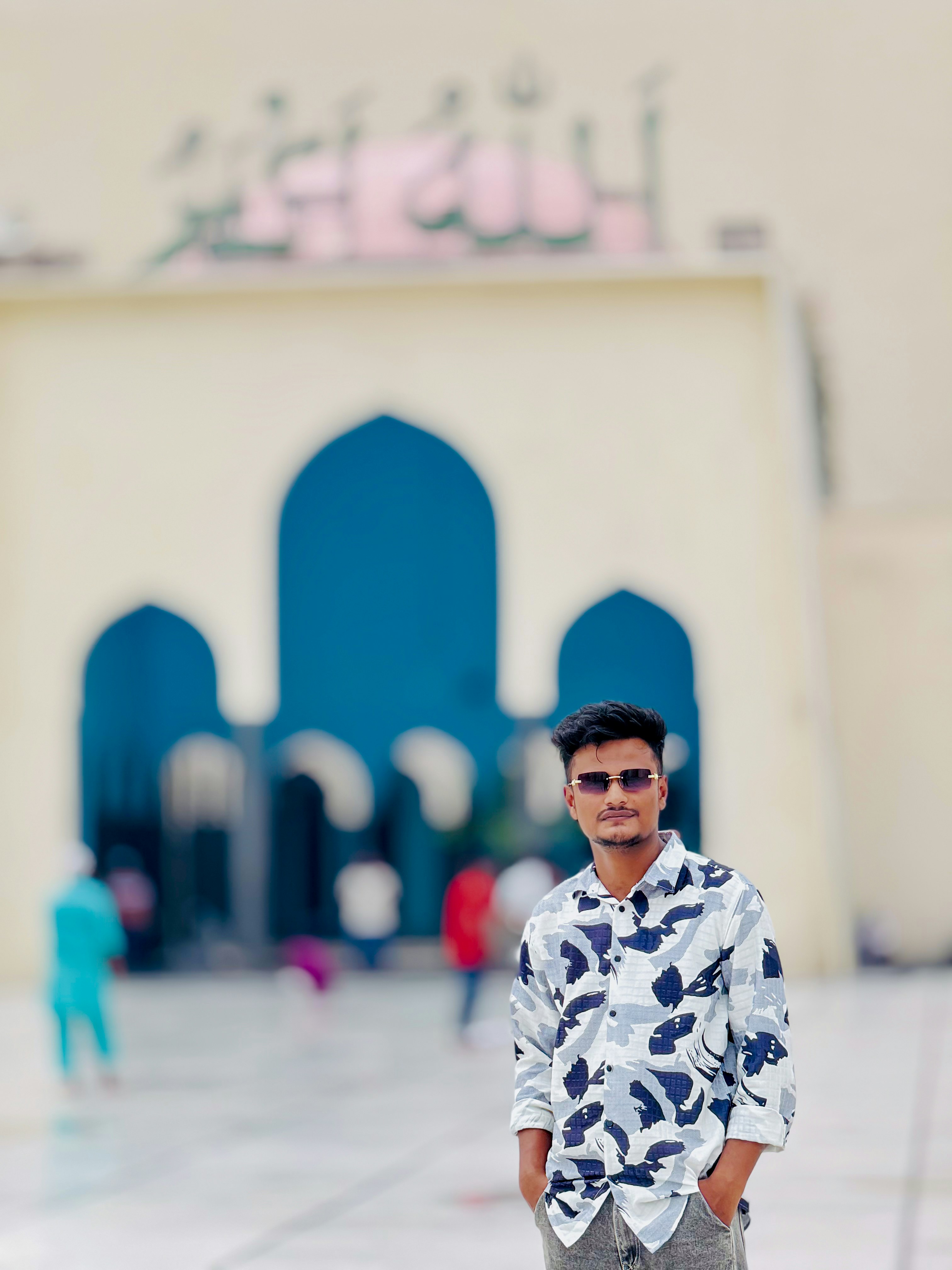 Stylish man in sunglasses stands before an arched building.