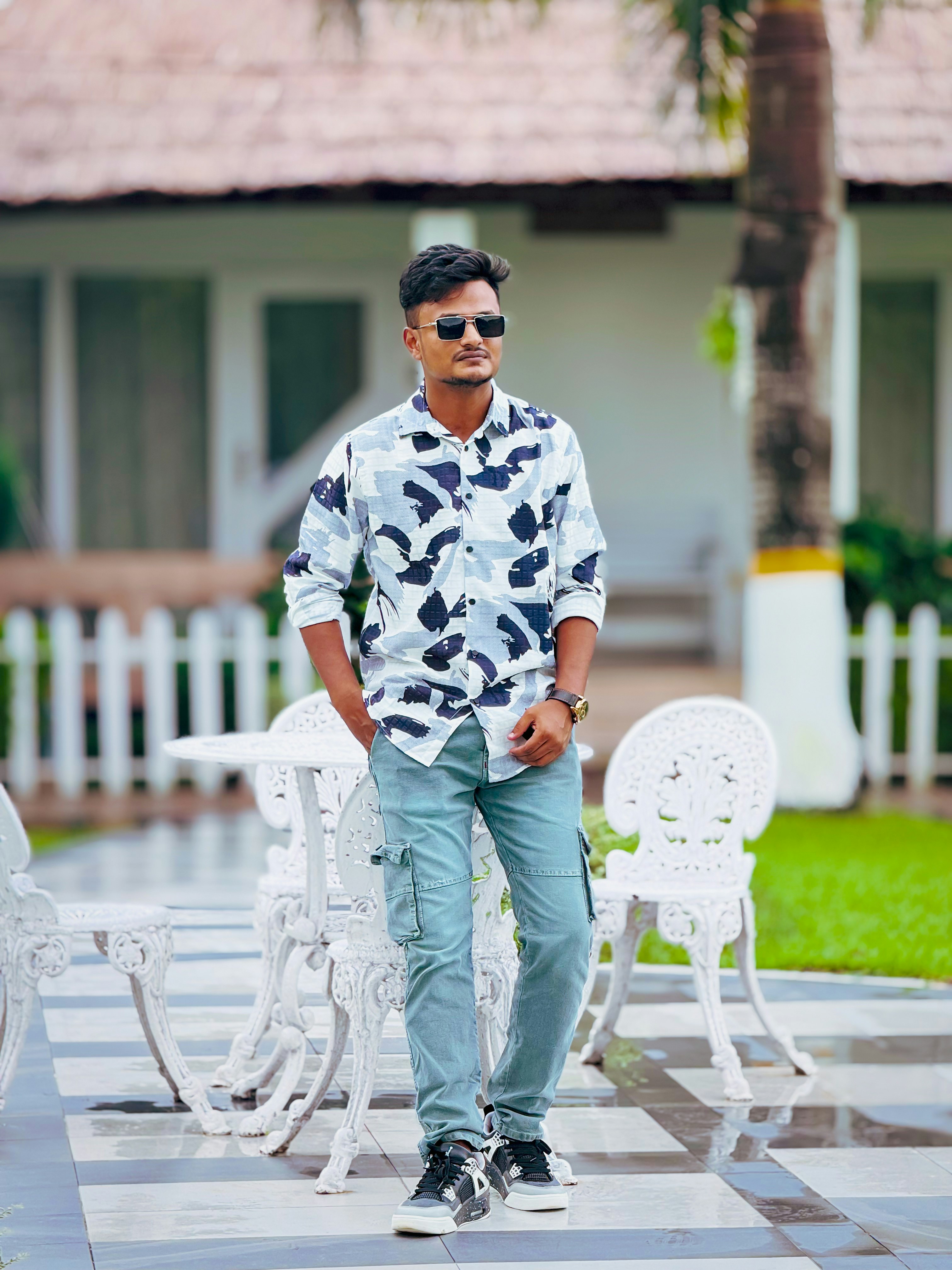 Man in patterned shirt and sunglasses stands outdoors.
