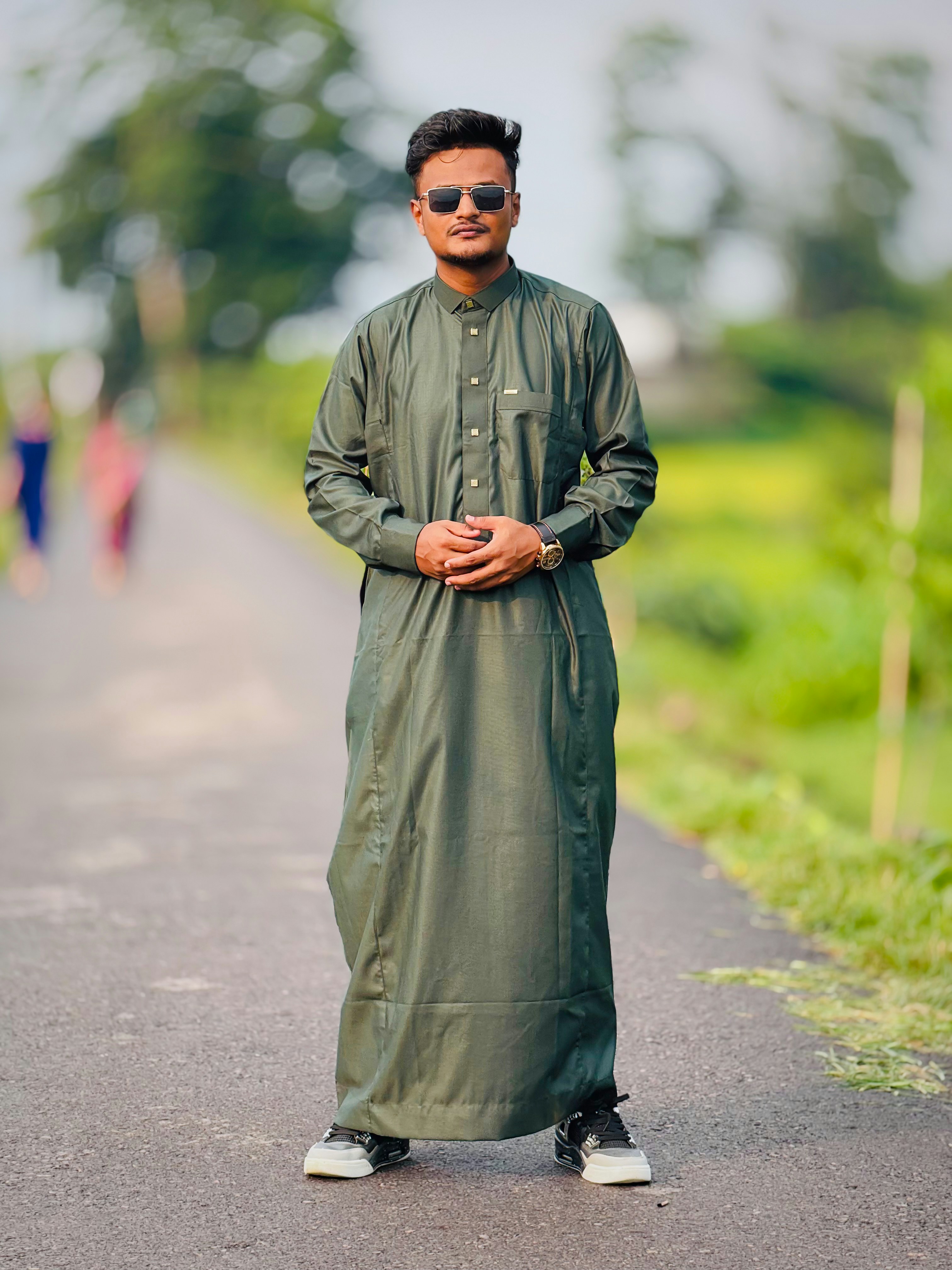Man wearing a long green tunic and sunglasses outdoors.
