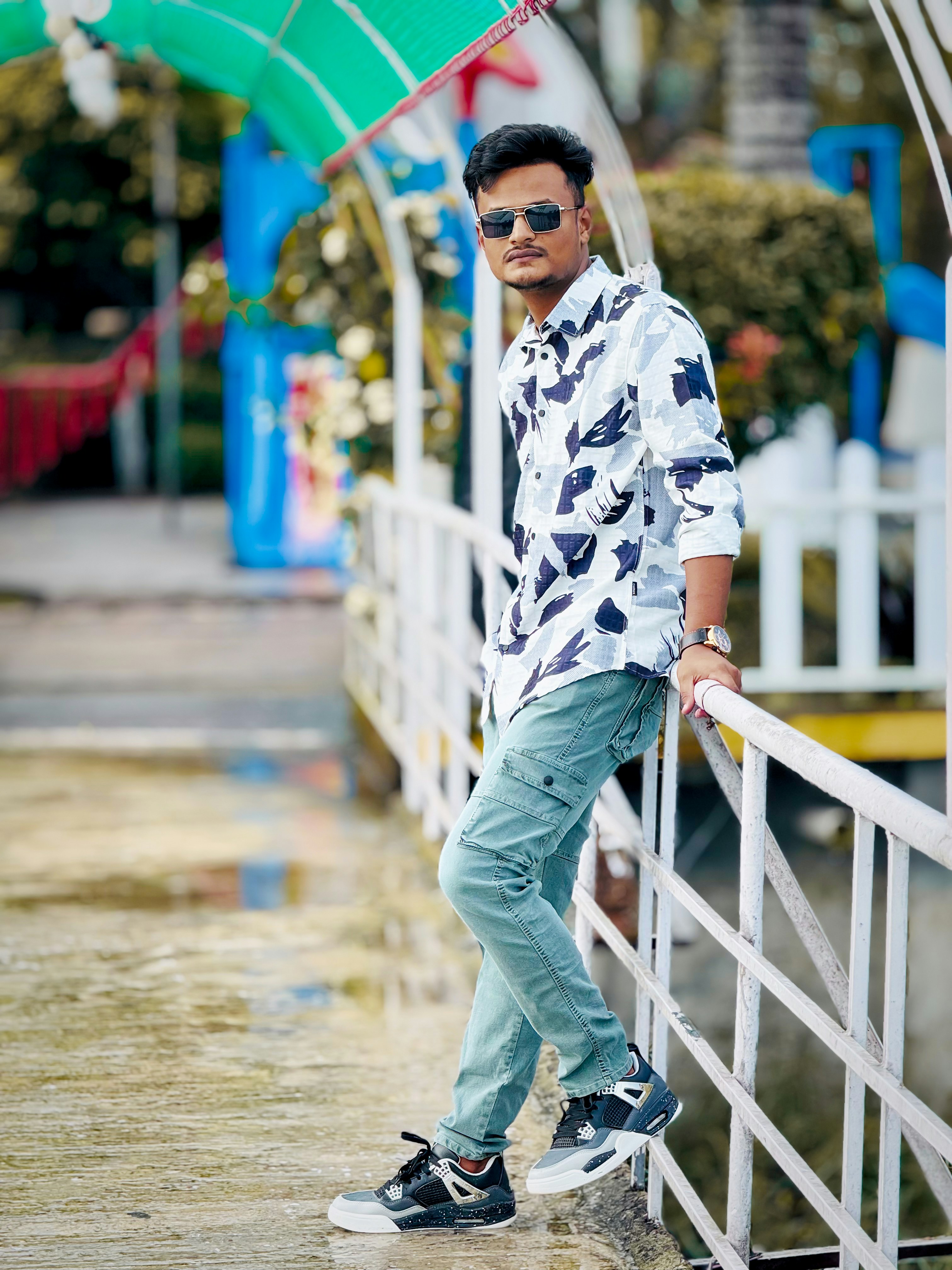 Stylish young man in sunglasses leaning on a bridge railing.