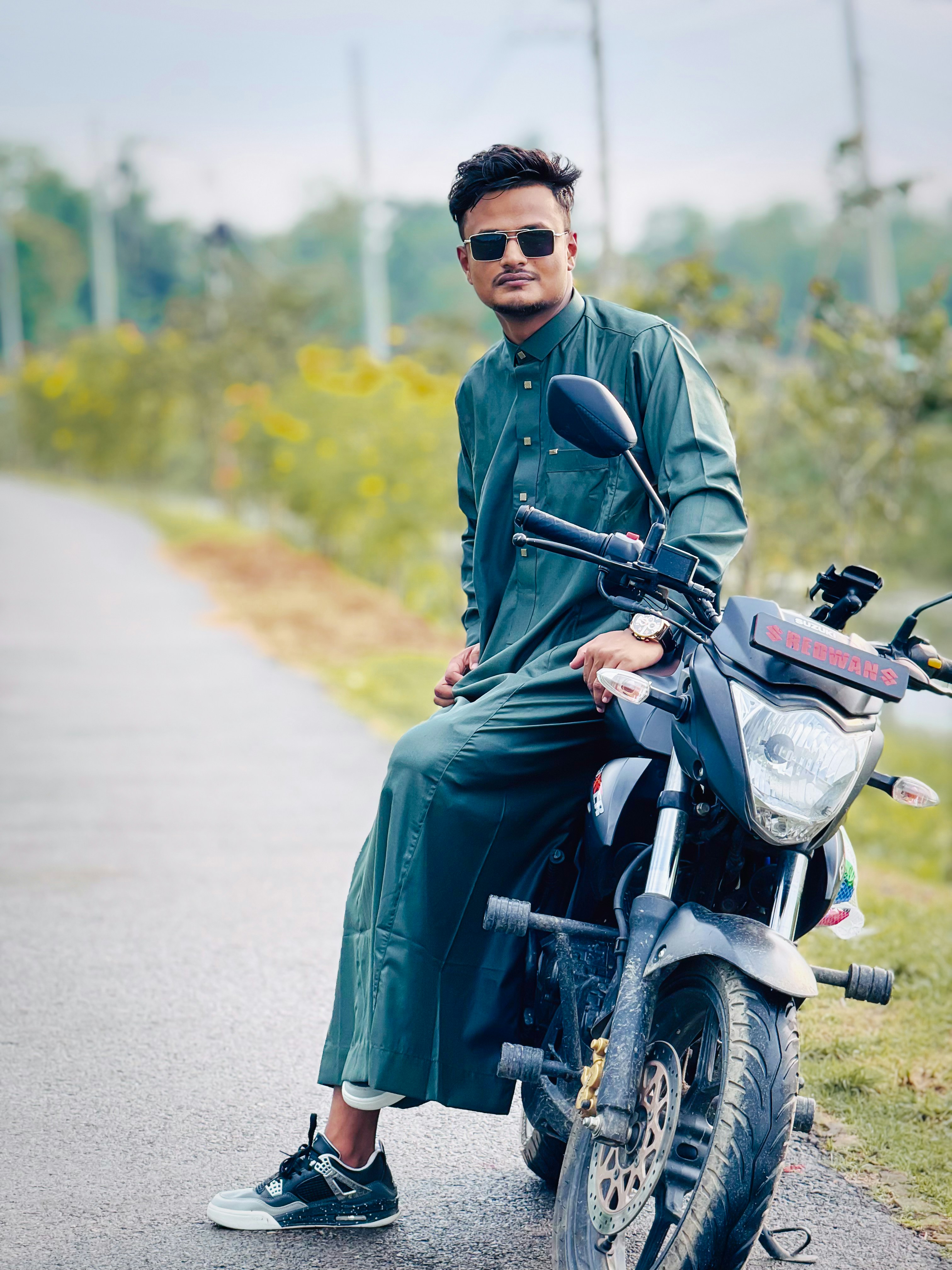 Young man in green traditional attire sitting on a motorcycle.