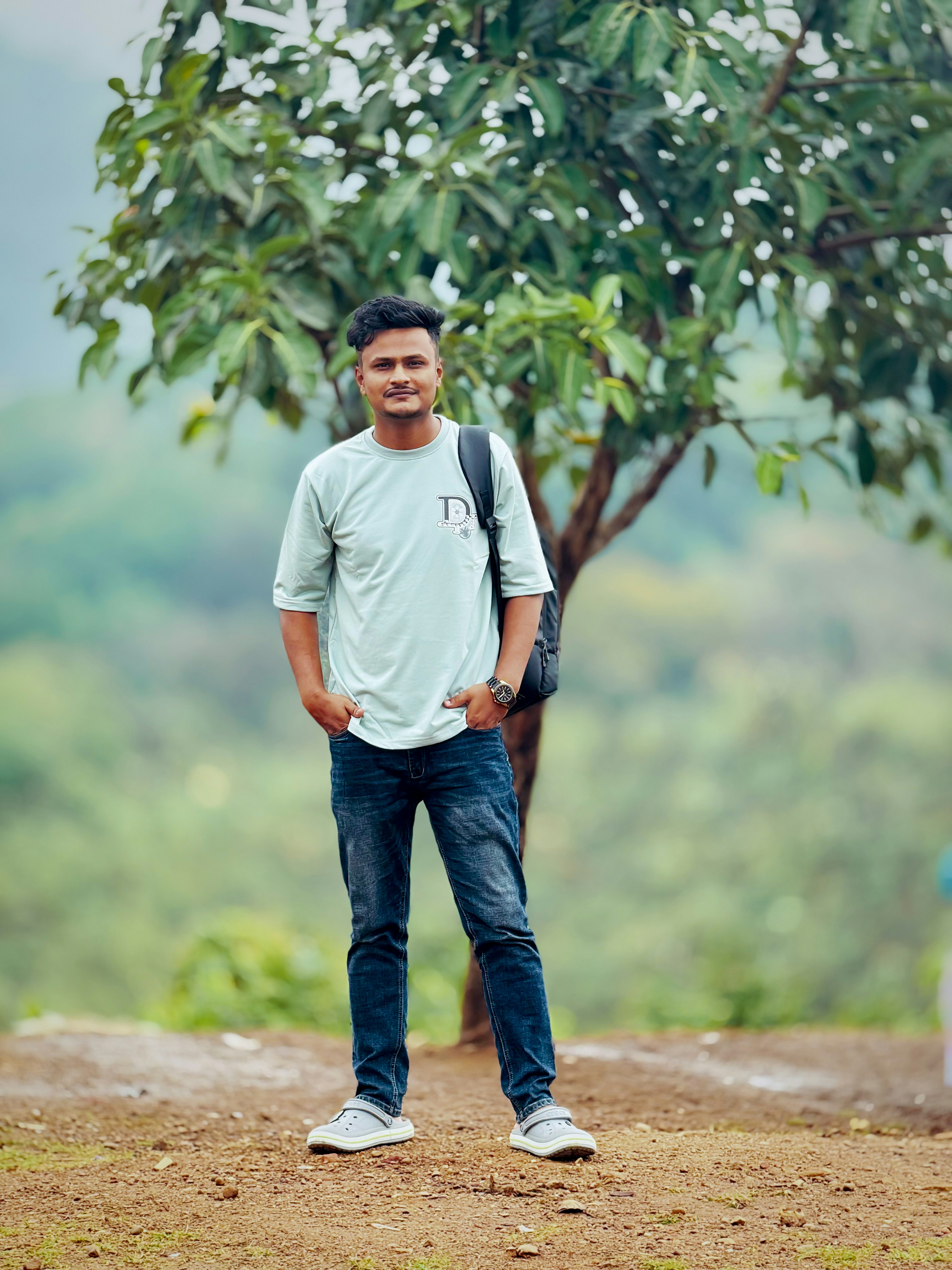 A young man standing outdoors with trees in the background.