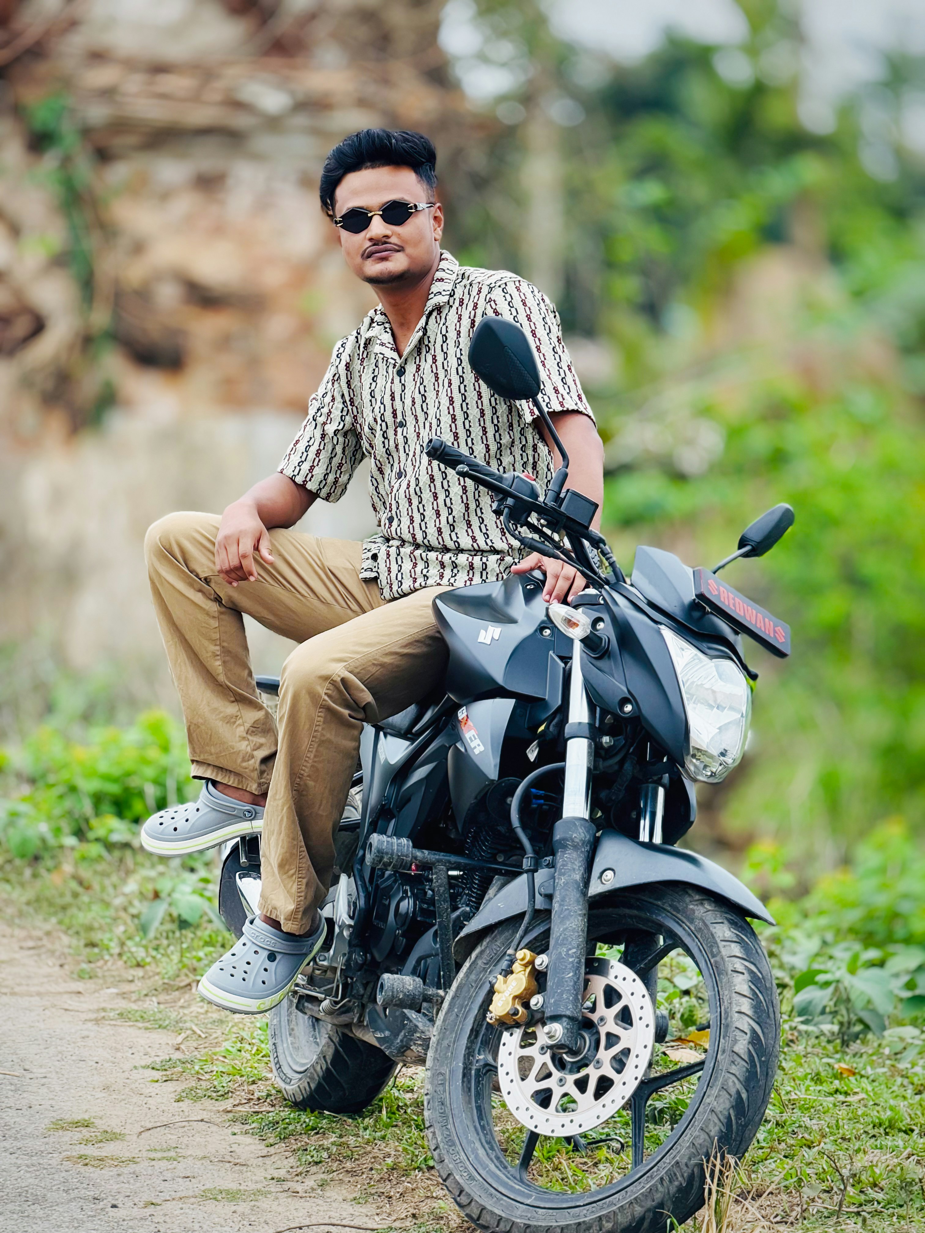 A young man wearing sunglasses sits on a motorcycle outdoors.