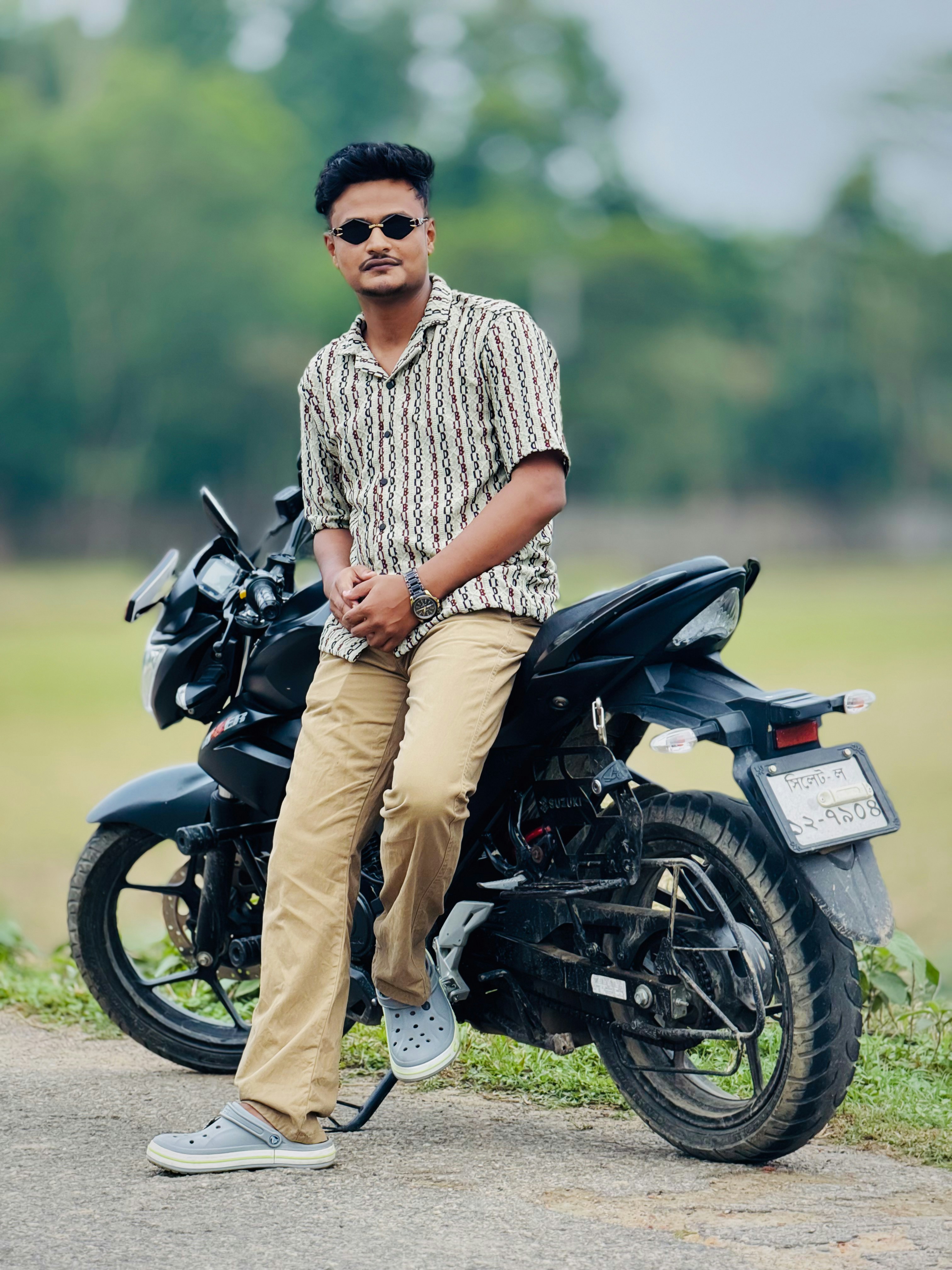 Young man in sunglasses leaning on a black motorcycle outdoors.