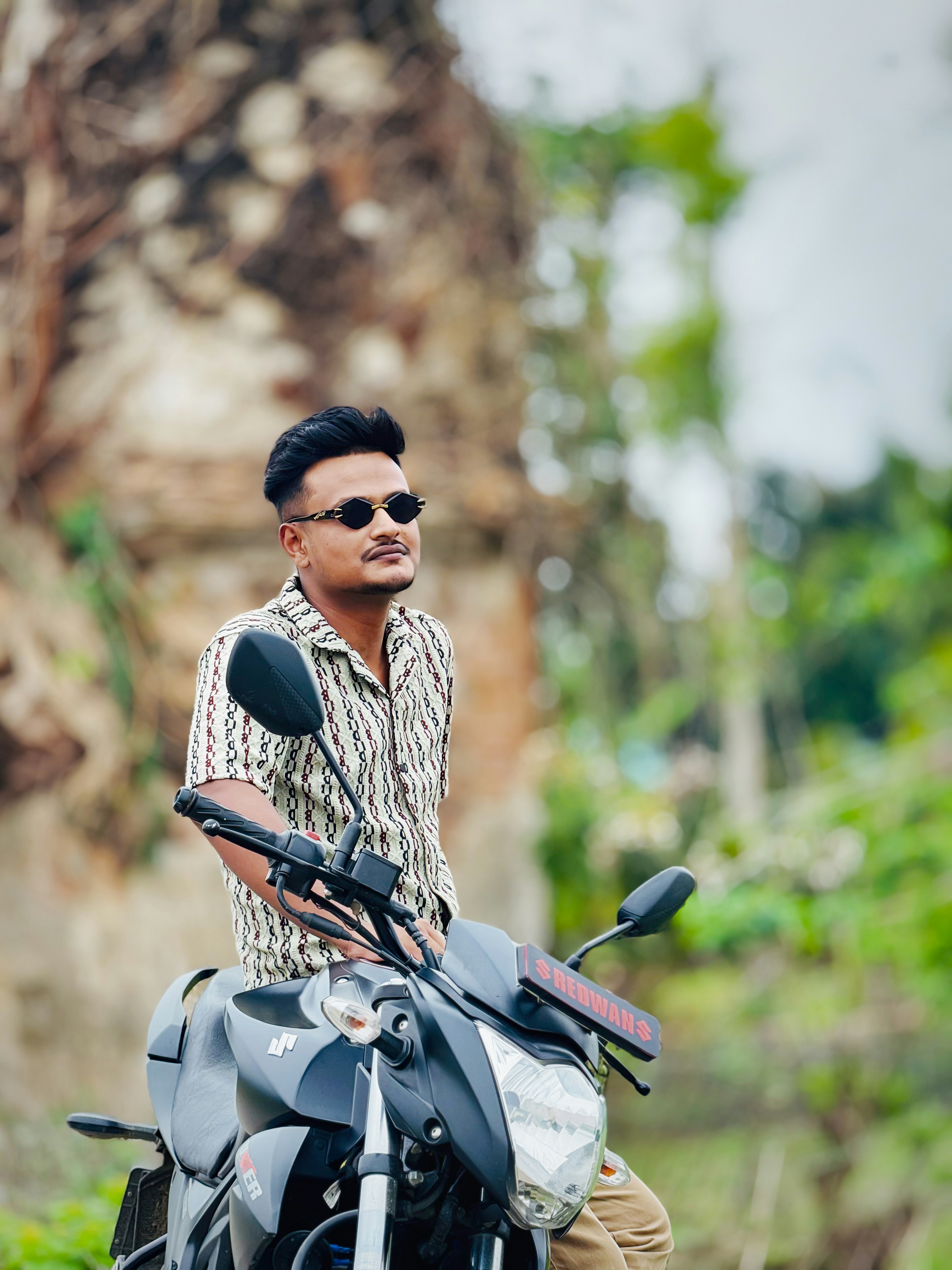 Young man in sunglasses sitting on a motorcycle outdoors.