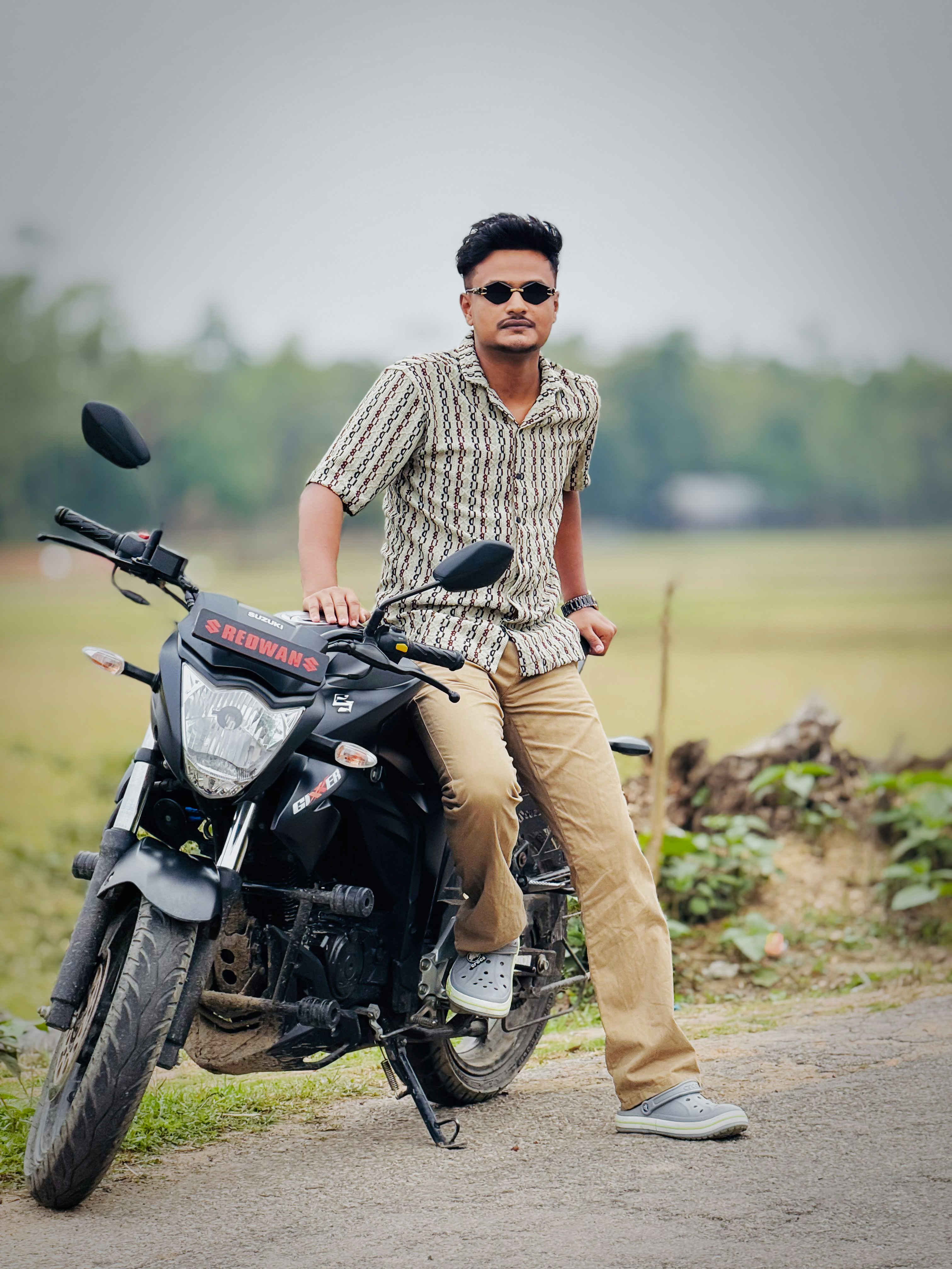 Young man in sunglasses standing beside a black motorcycle.