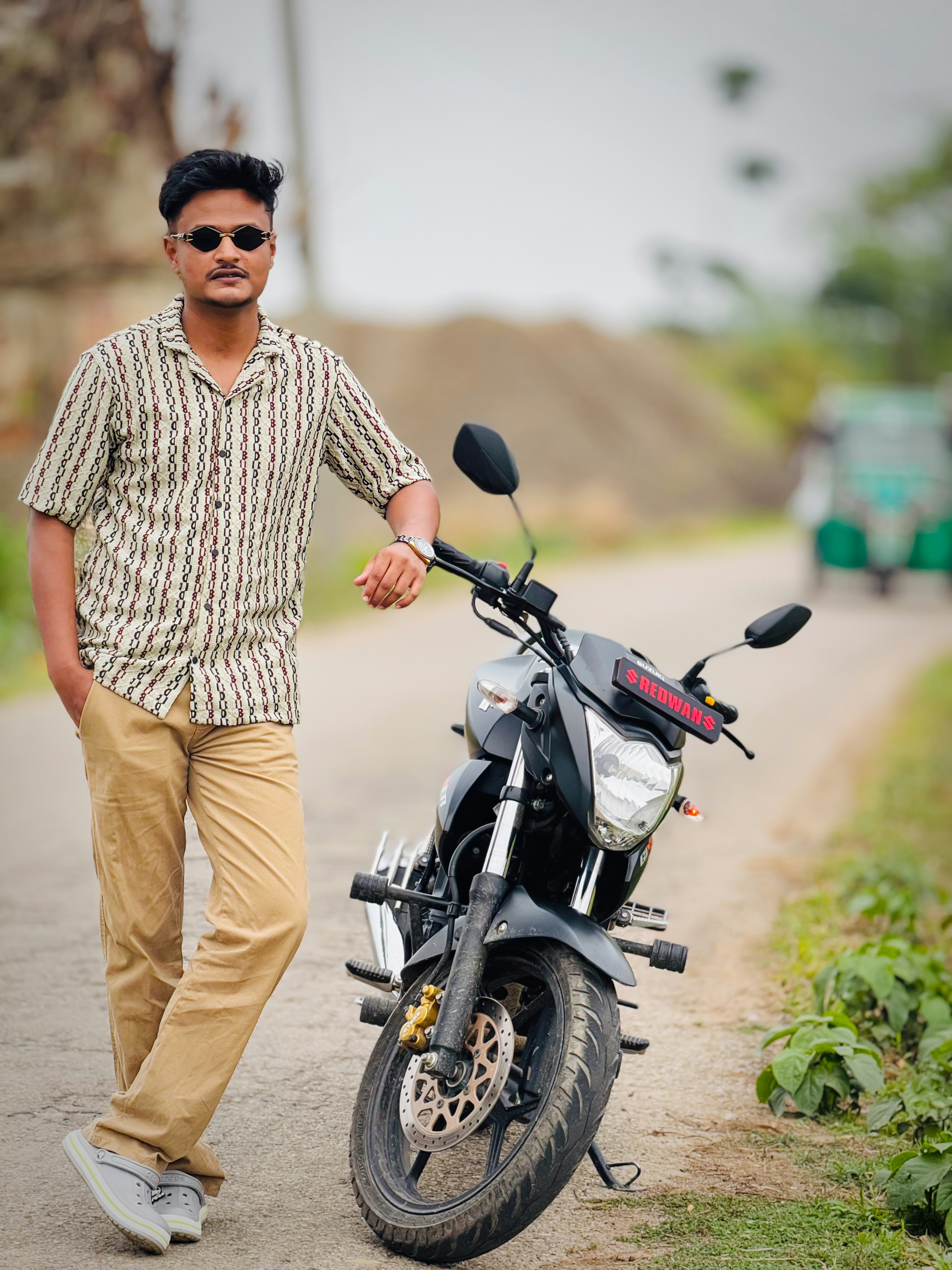 Young man in sunglasses poses with his motorcycle outdoors.