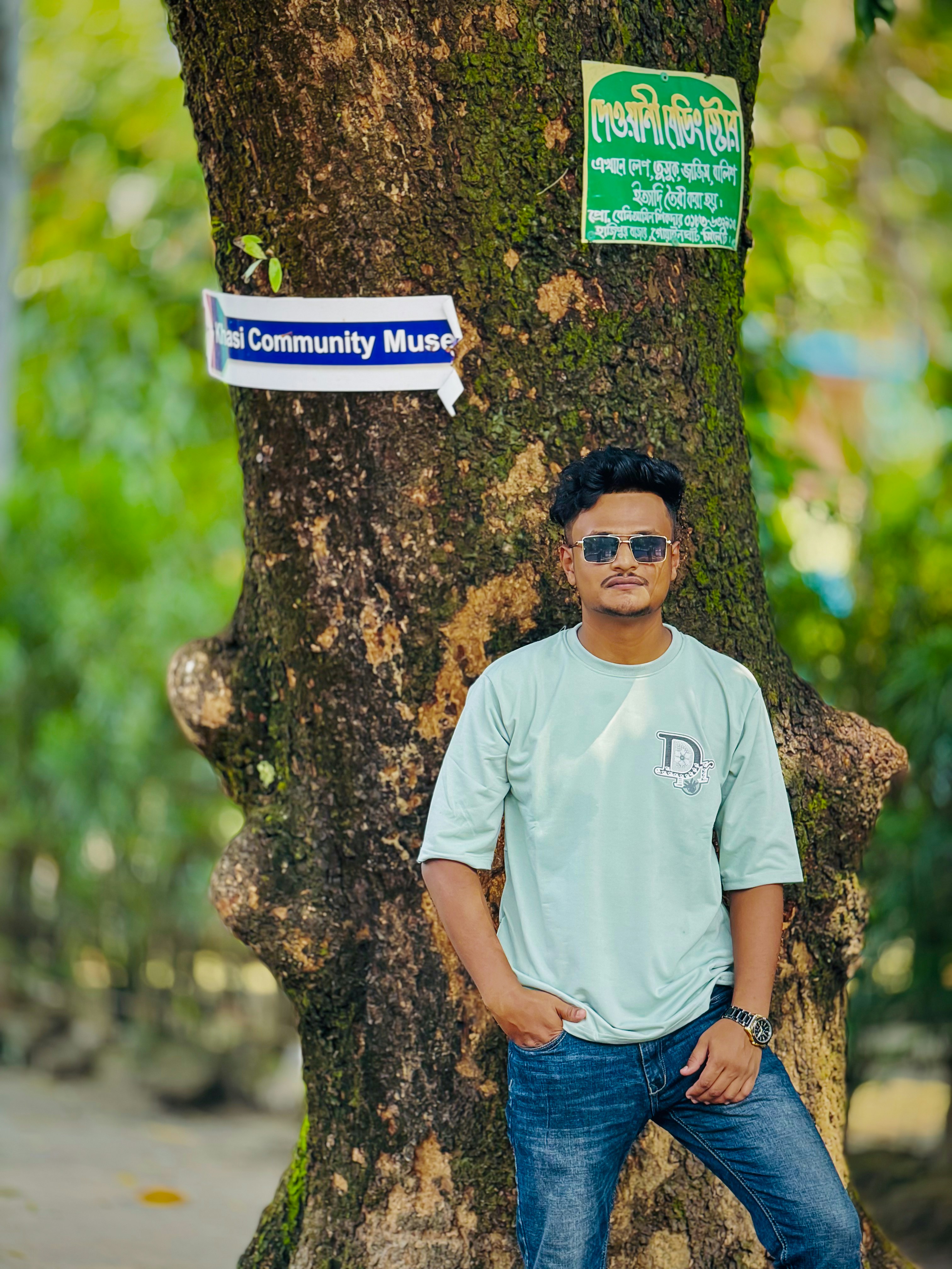 Man in sunglasses stands beside a large tree.