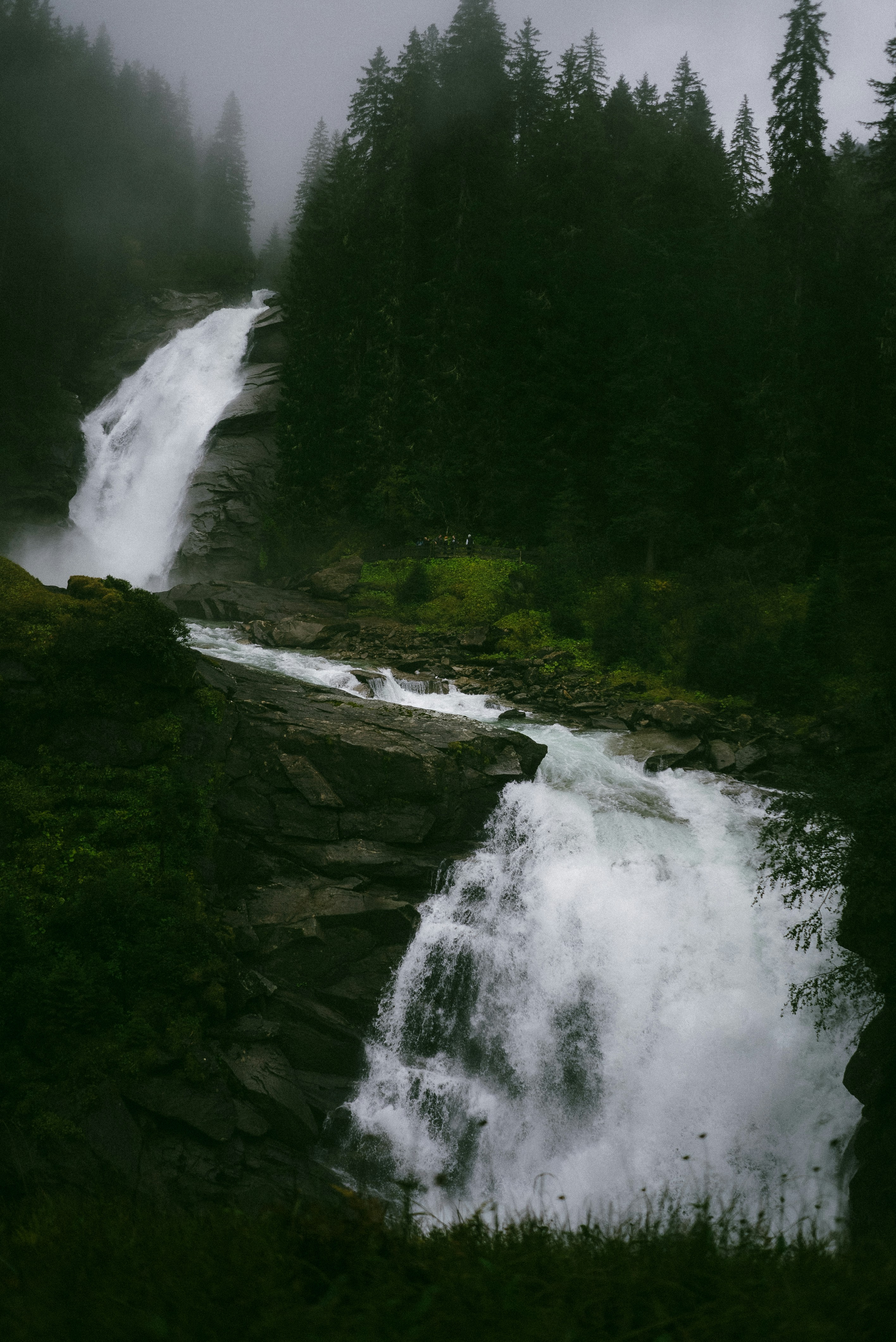 Multi-tiered waterfall tumbles down a rocky, forested mountain.