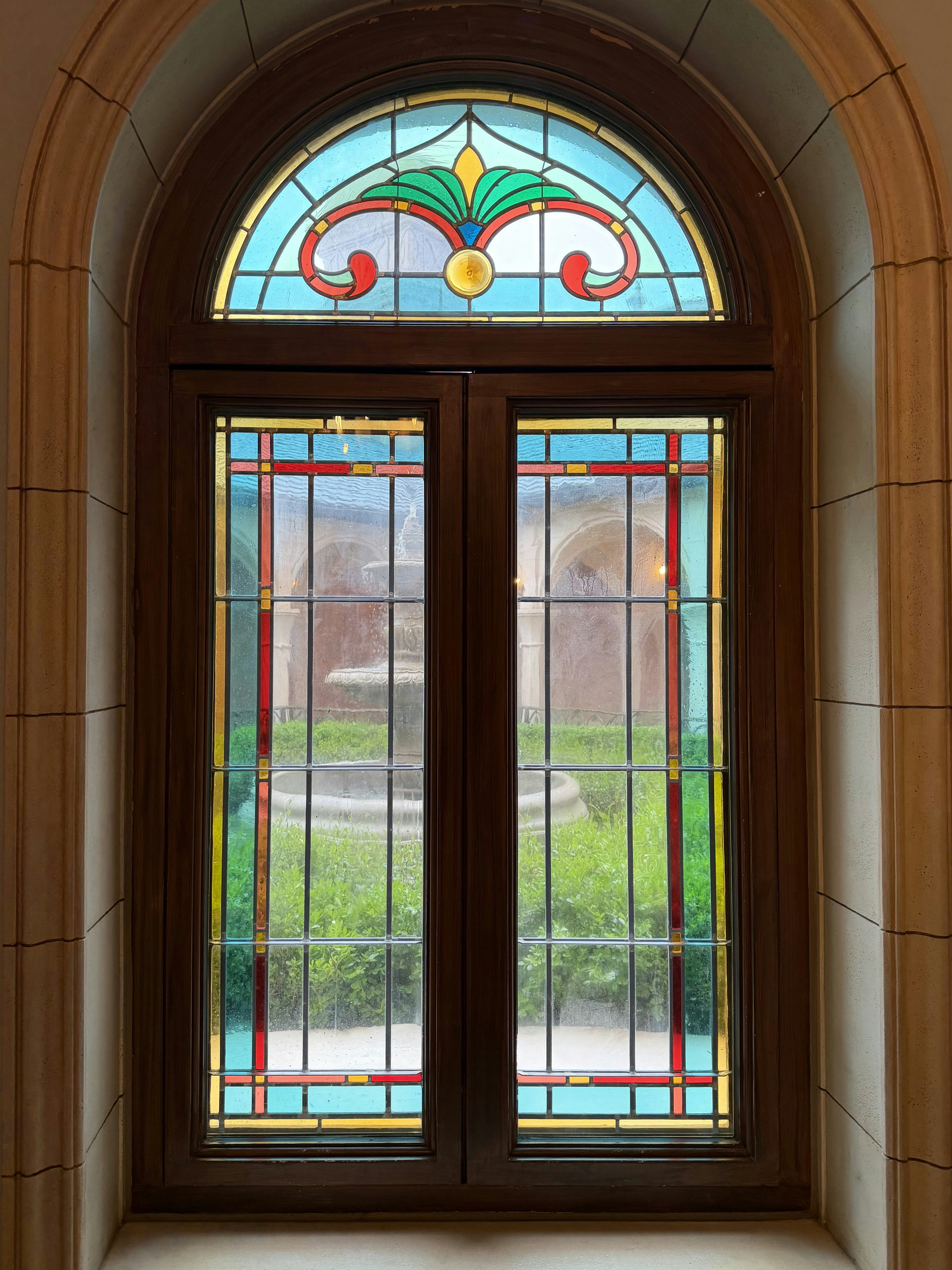 A colorful stained glass window frames a peaceful courtyard beyond.