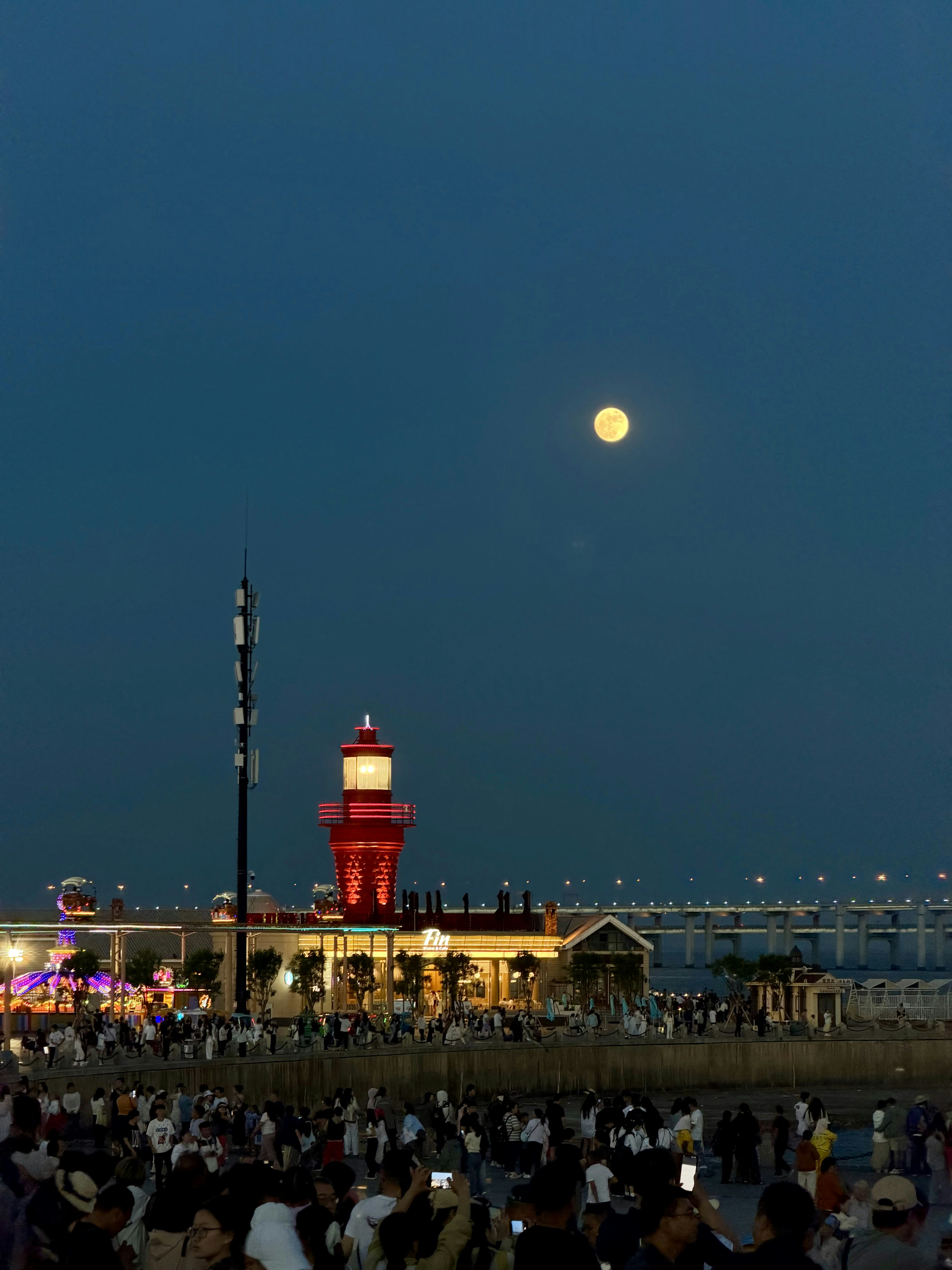 Moonlit Pier: Red Lighthouse Amid a Sea of Nightlife
