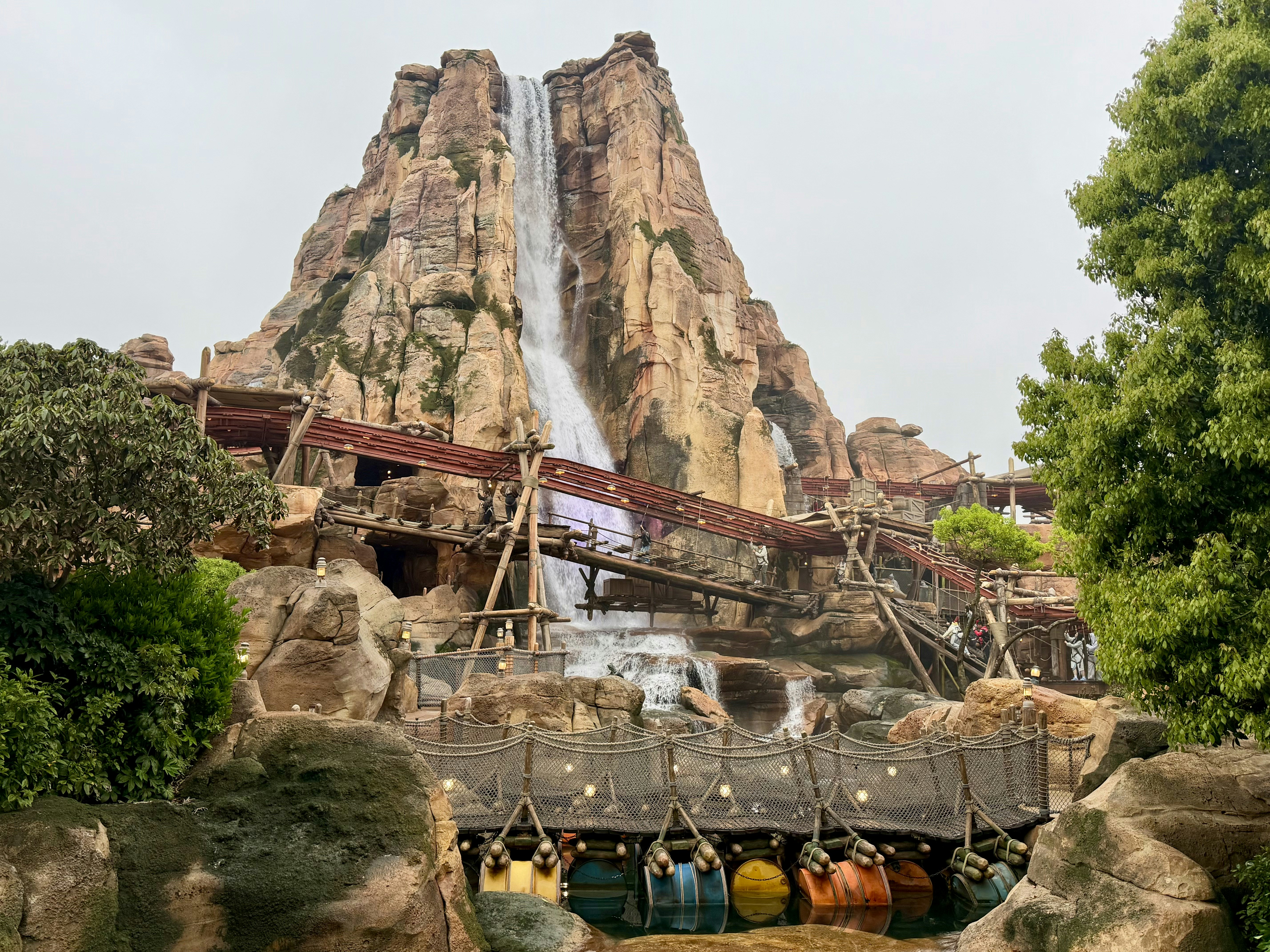 A dramatic mountain landscape and cascading waterfall create an adventurous theme park scene.