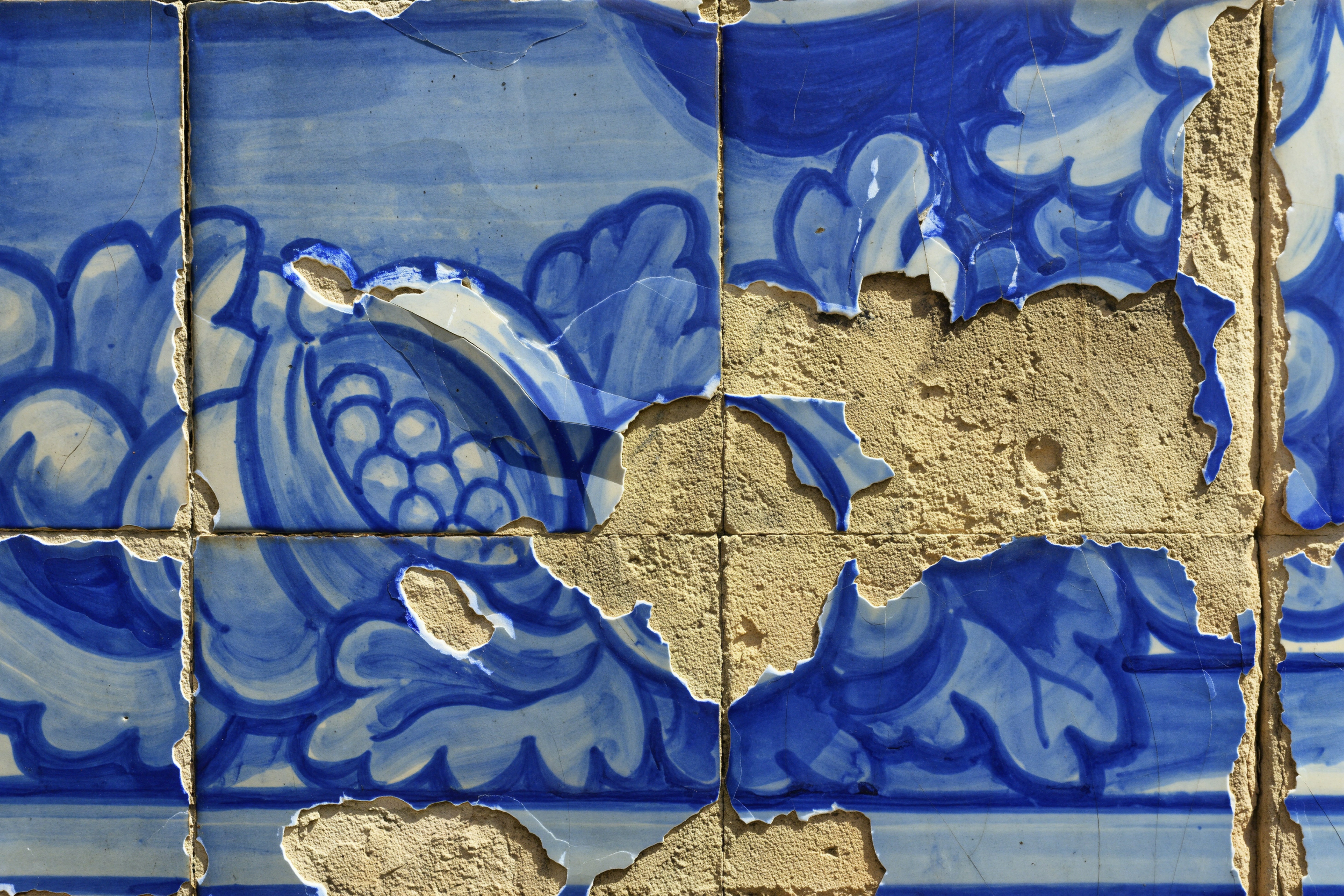 Old blue tile wall with missing pieces shows time's effect on the surface and design in a historic building in a city - Pieces of blue tiles are missing from the wall, revealing the rough texture underneath. This wall shows the wear over many years in a place with history and charm.