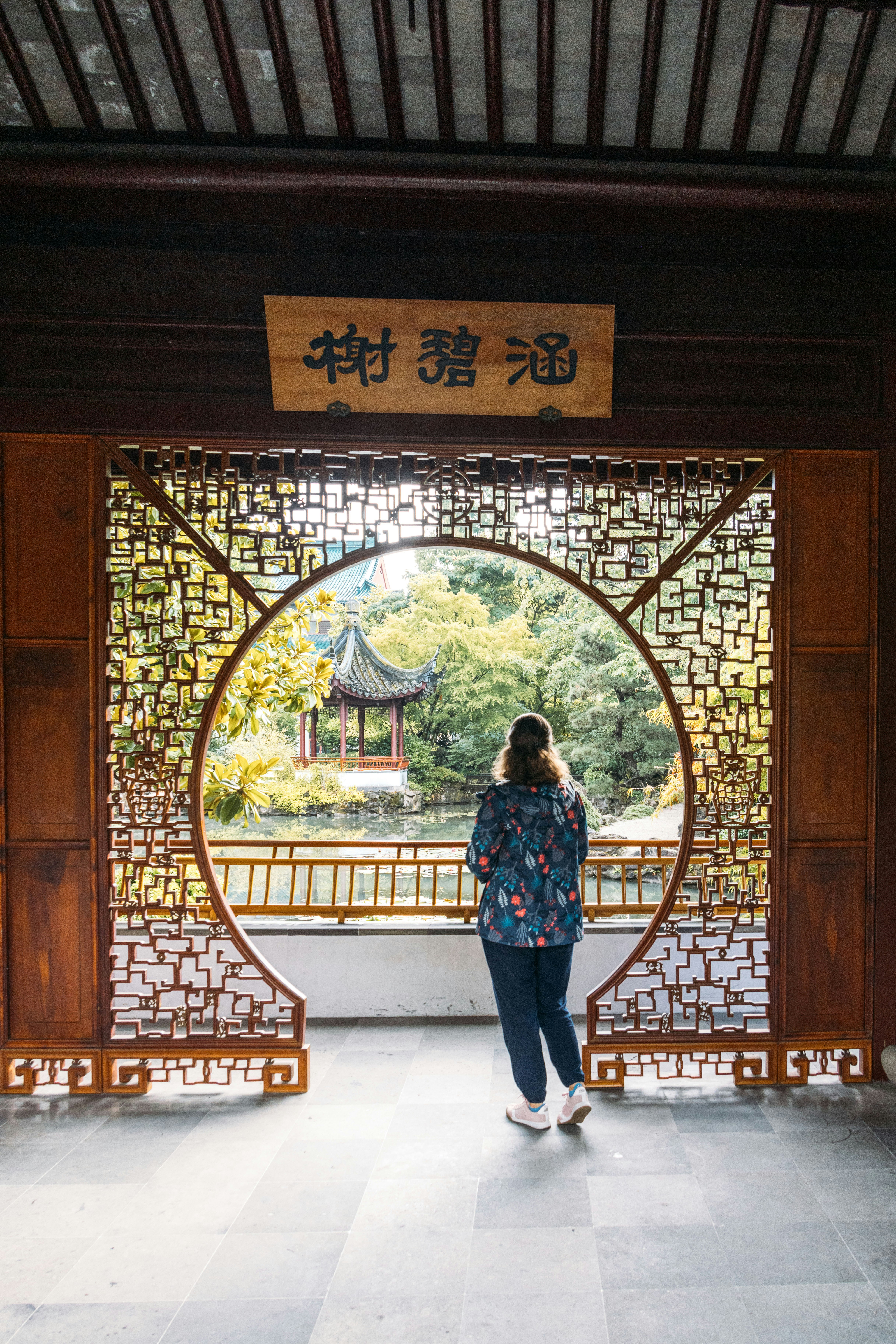 Traveler in a Circular Gate Overlooking a Tranquil Chinese Garden