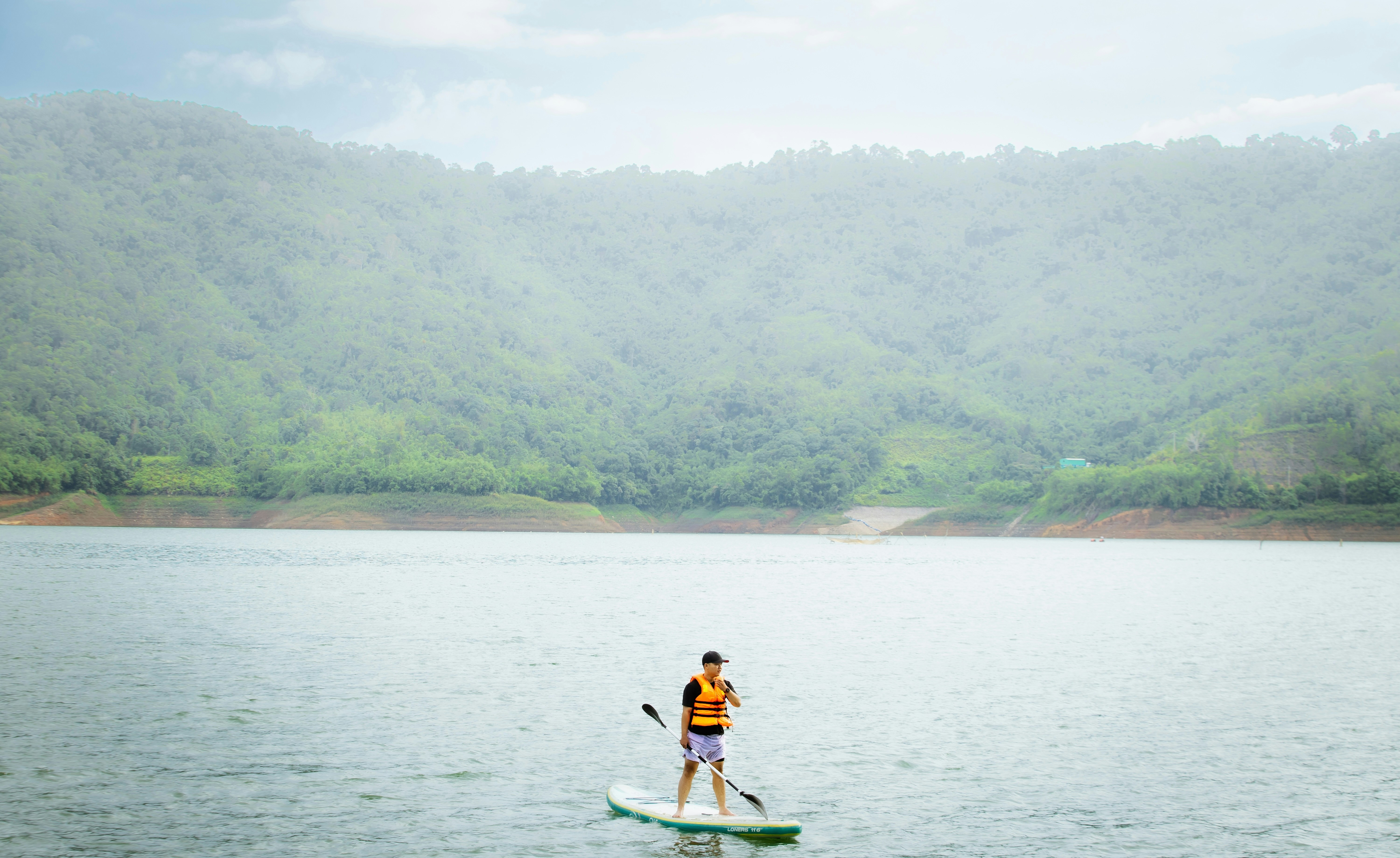 Surfer on a Quiet Lake: Solo Figure Amid Misty Hills