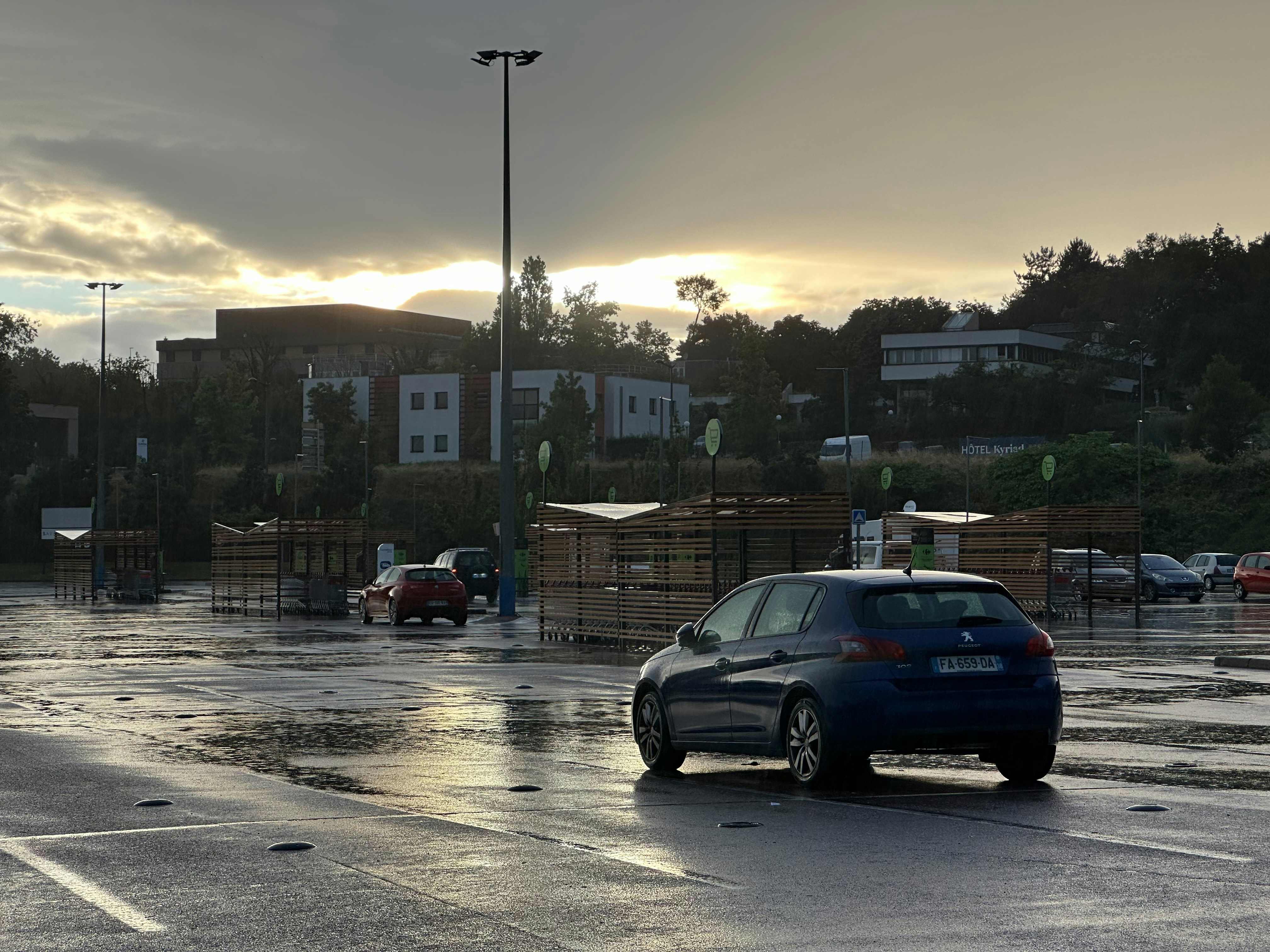 Blue Hatchback in a Reflective Parking Lot at Sunset