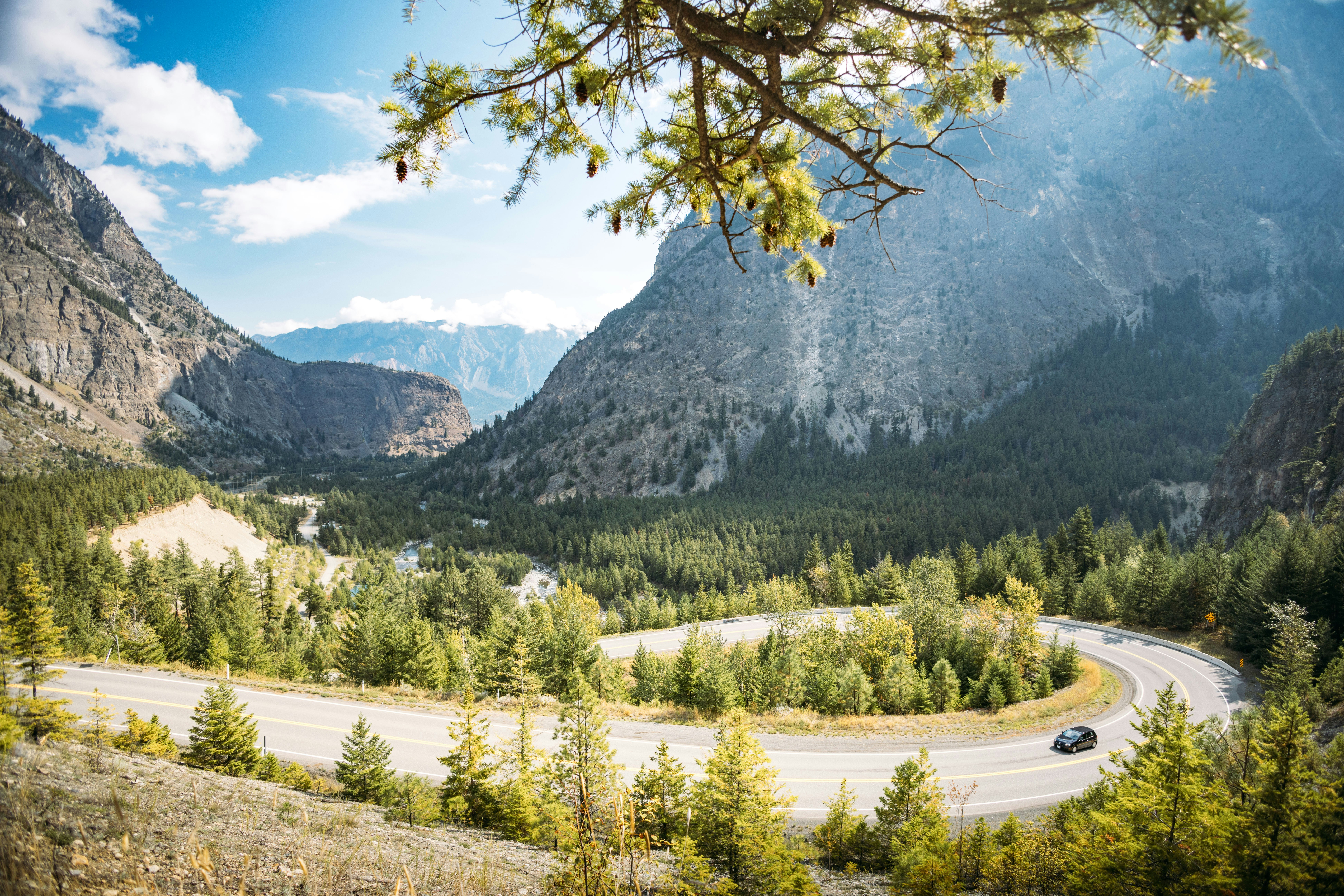 A winding road through a mountainous forest with a car.