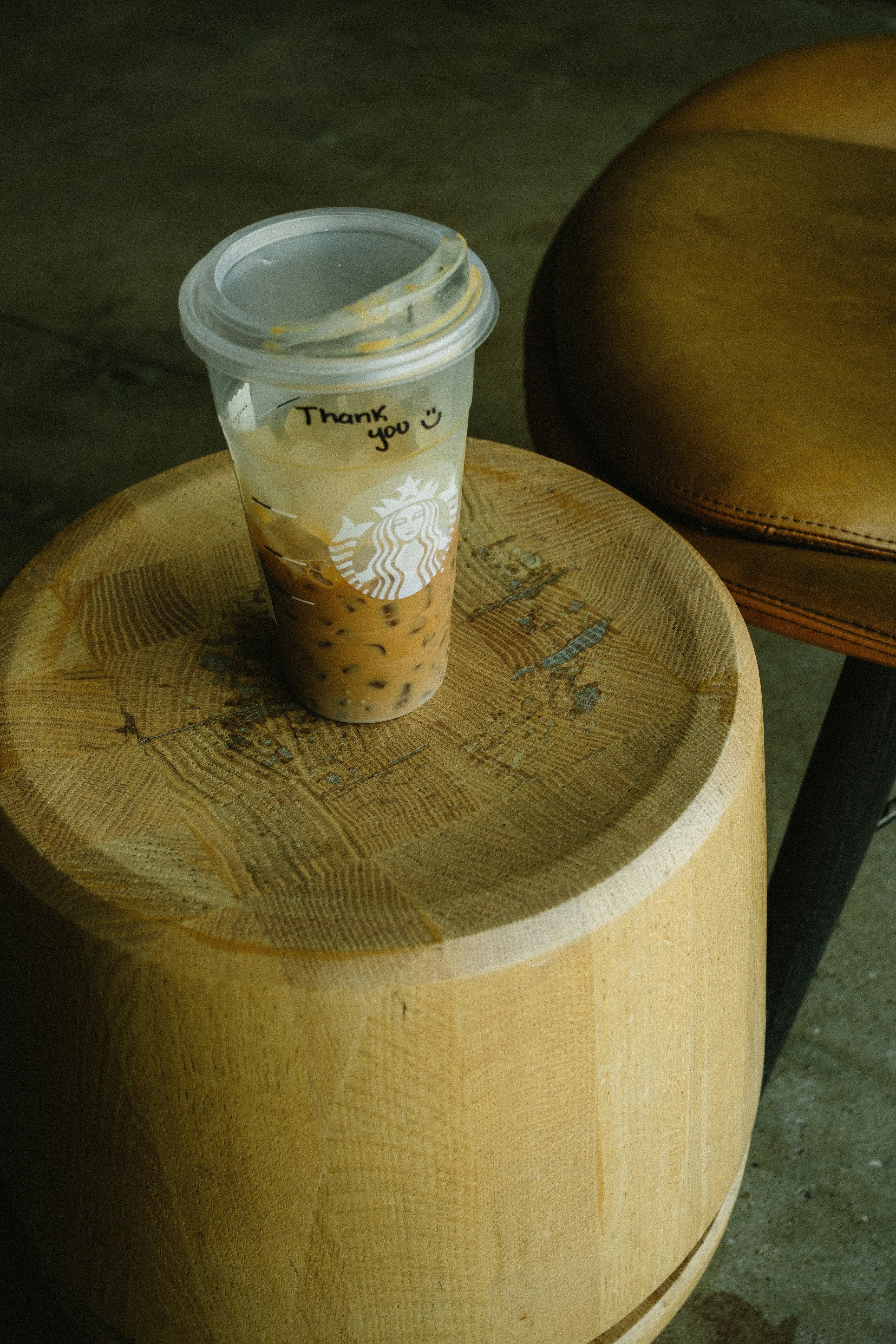 Iced coffee cup with "thank you" on a wooden stool.
