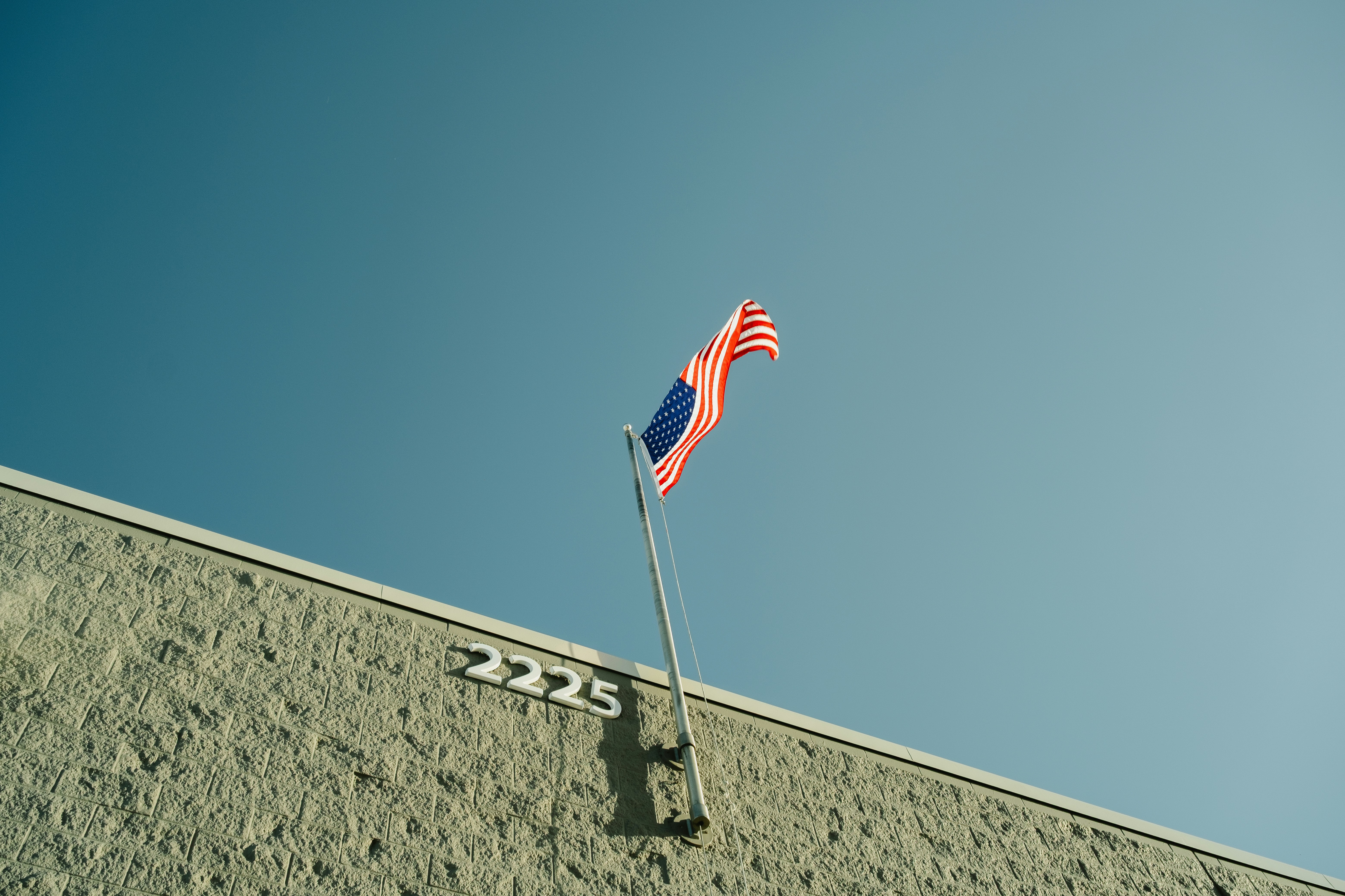 Us flag on a building under a blue sky.