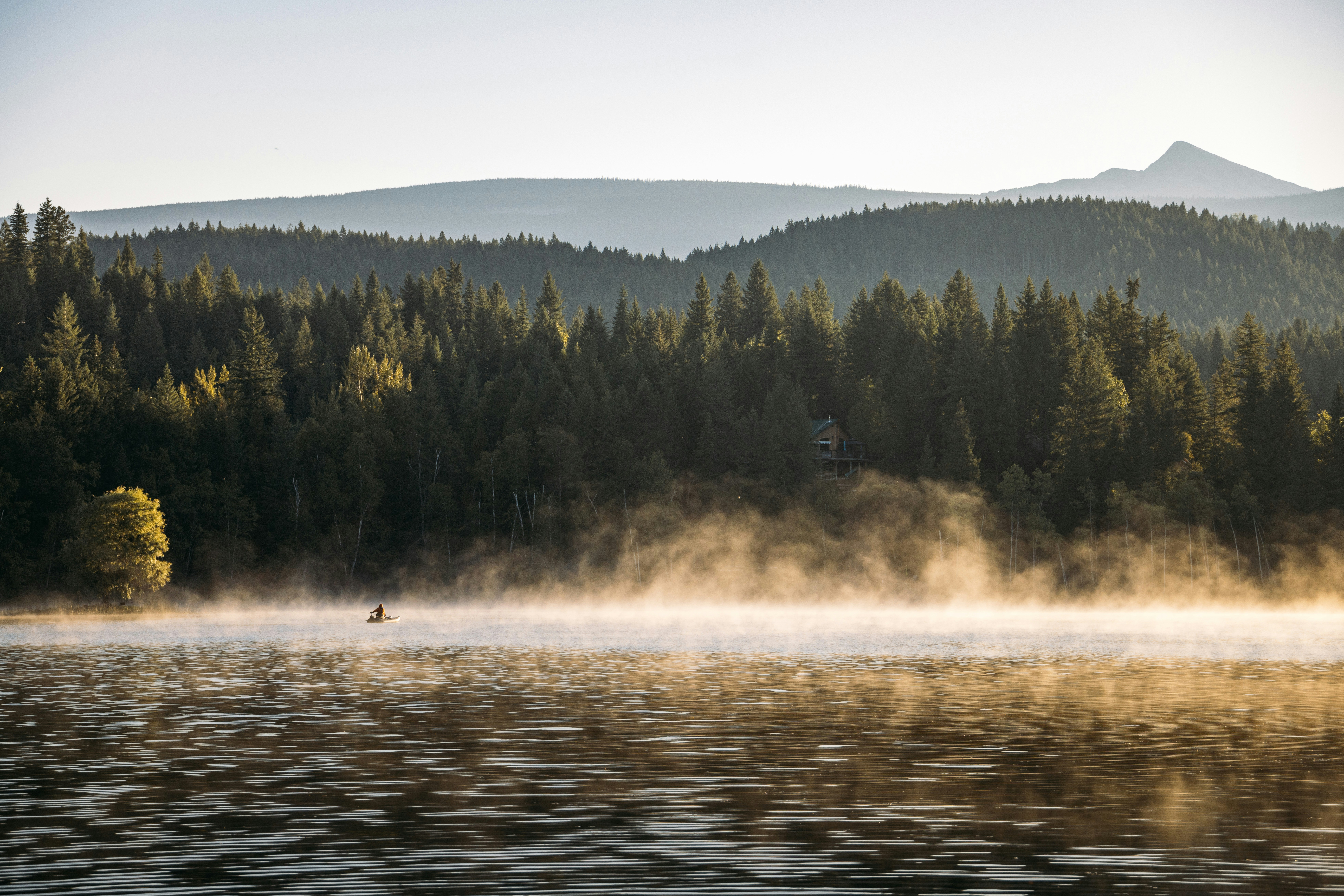 Sunrise mist over a tranquil lake with forests and mountains.