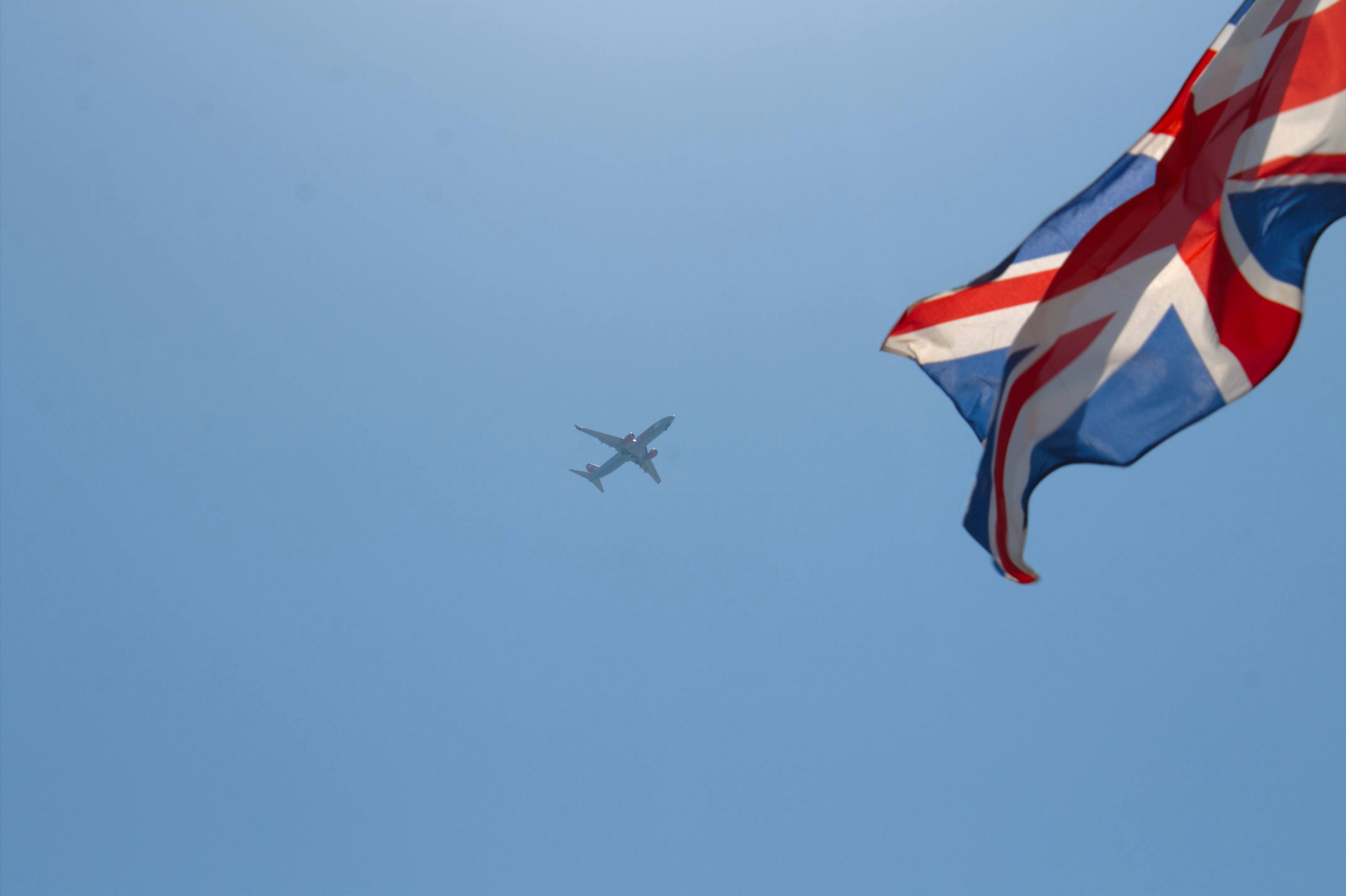 Winged Transit: A Jet Crossing a Solemn Sky beside a fluttering Union Flag