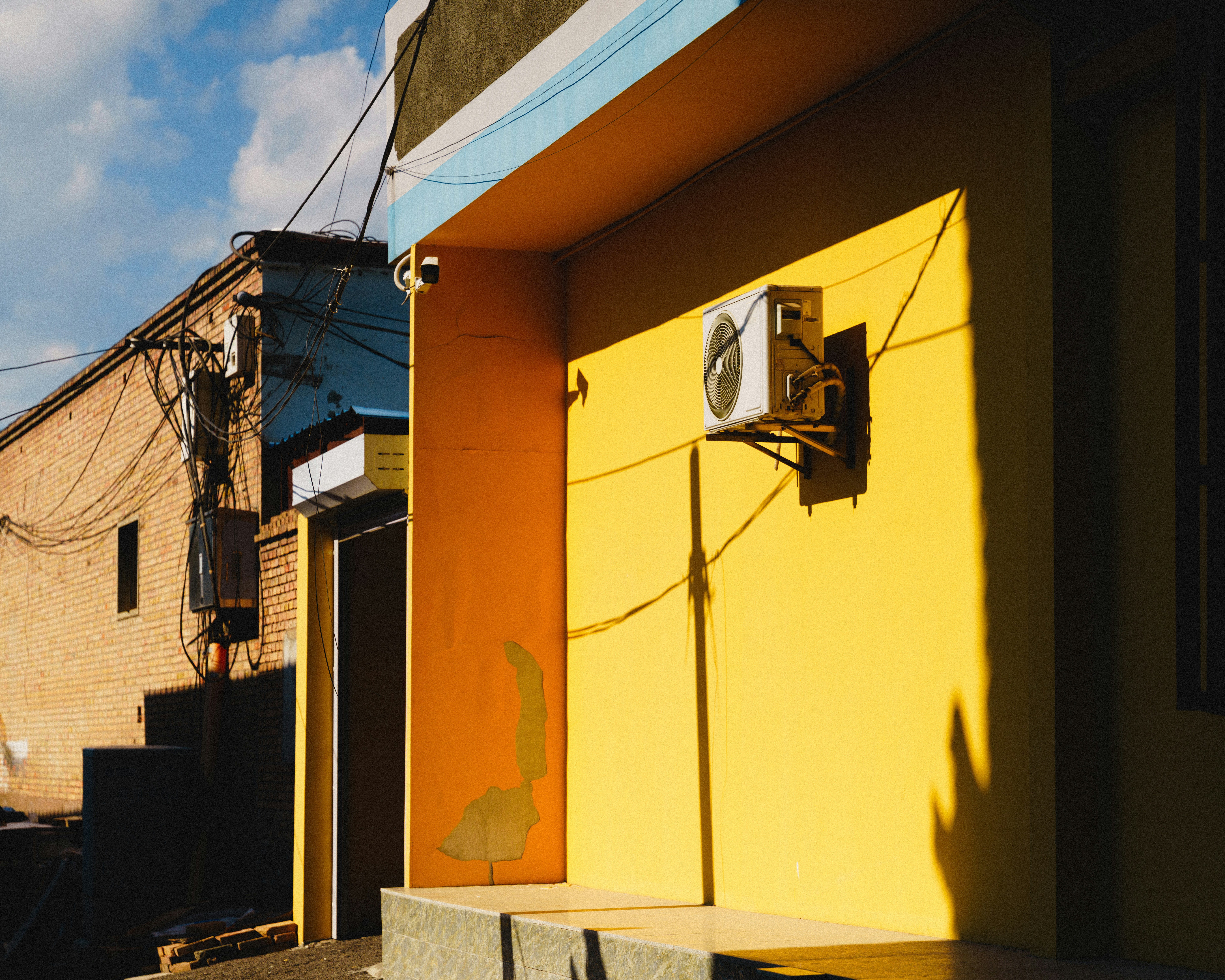 Sunlit Yellow Wall and Air Conditioner: Shadows in an Alleyway