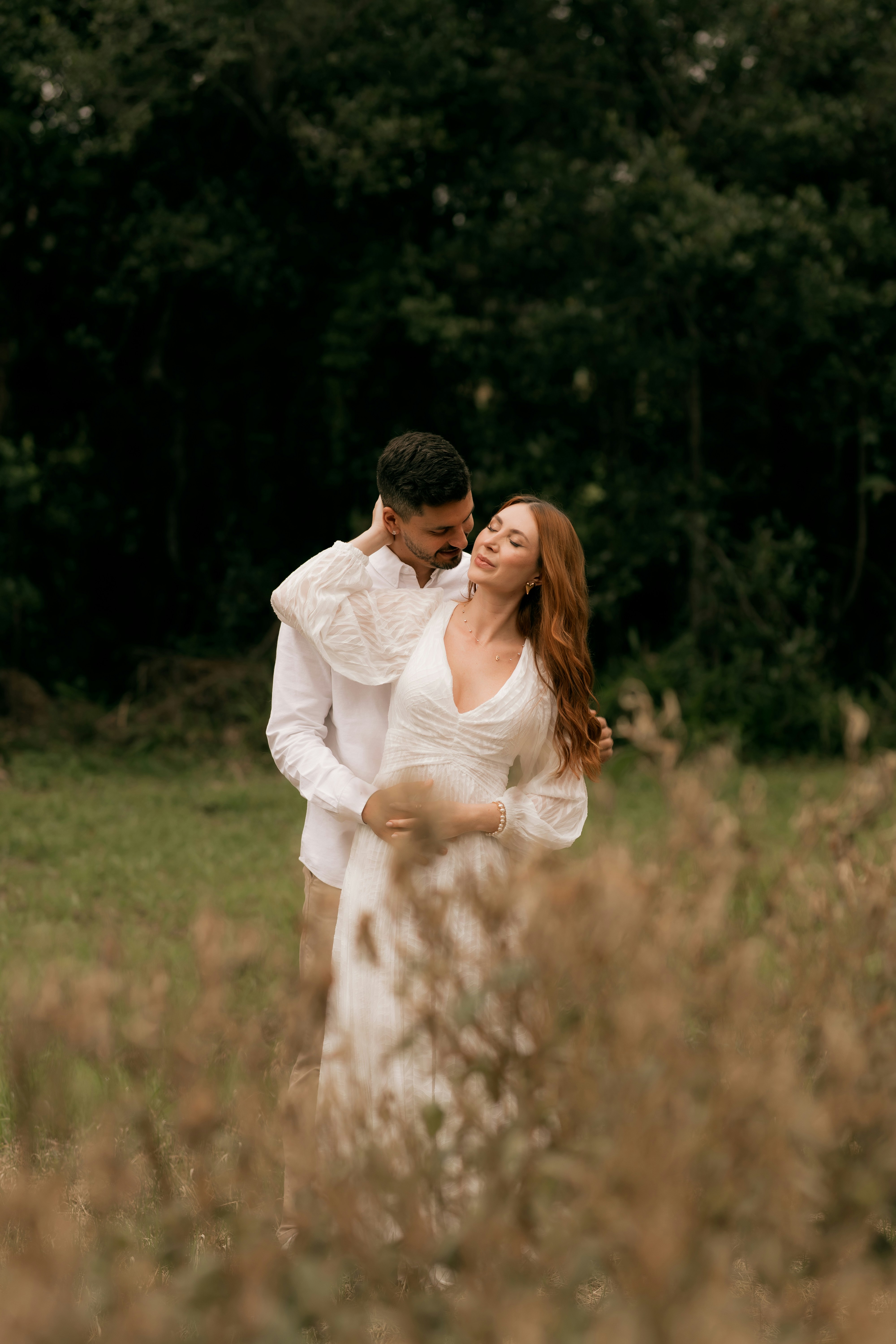 A couple embracing in a field with tall grasses.